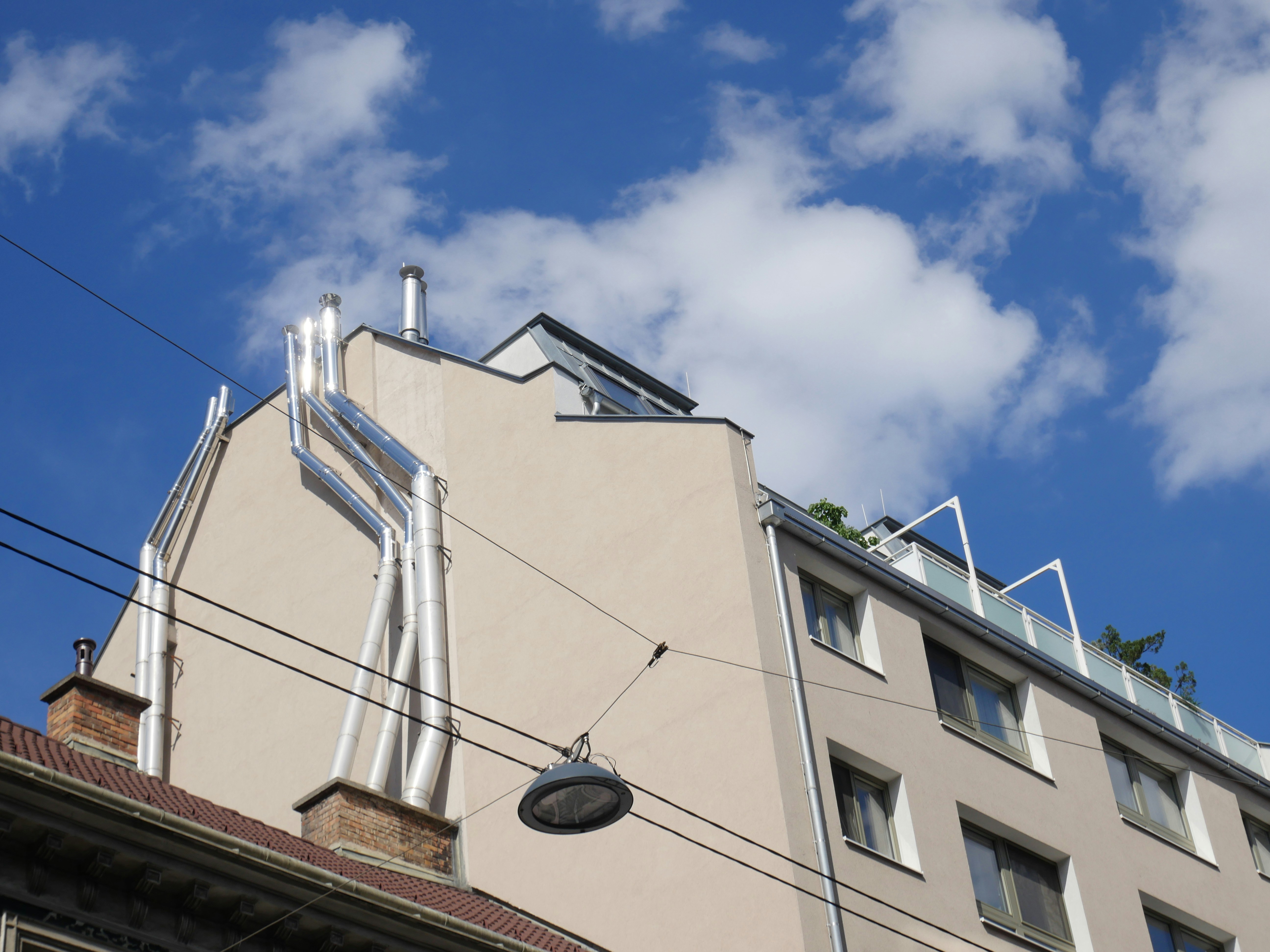 Multistory building with exposed metallic pipes and a curved street lamp under a bright blue sky. The scene emphasizes urban architecture and utility infrastructure.