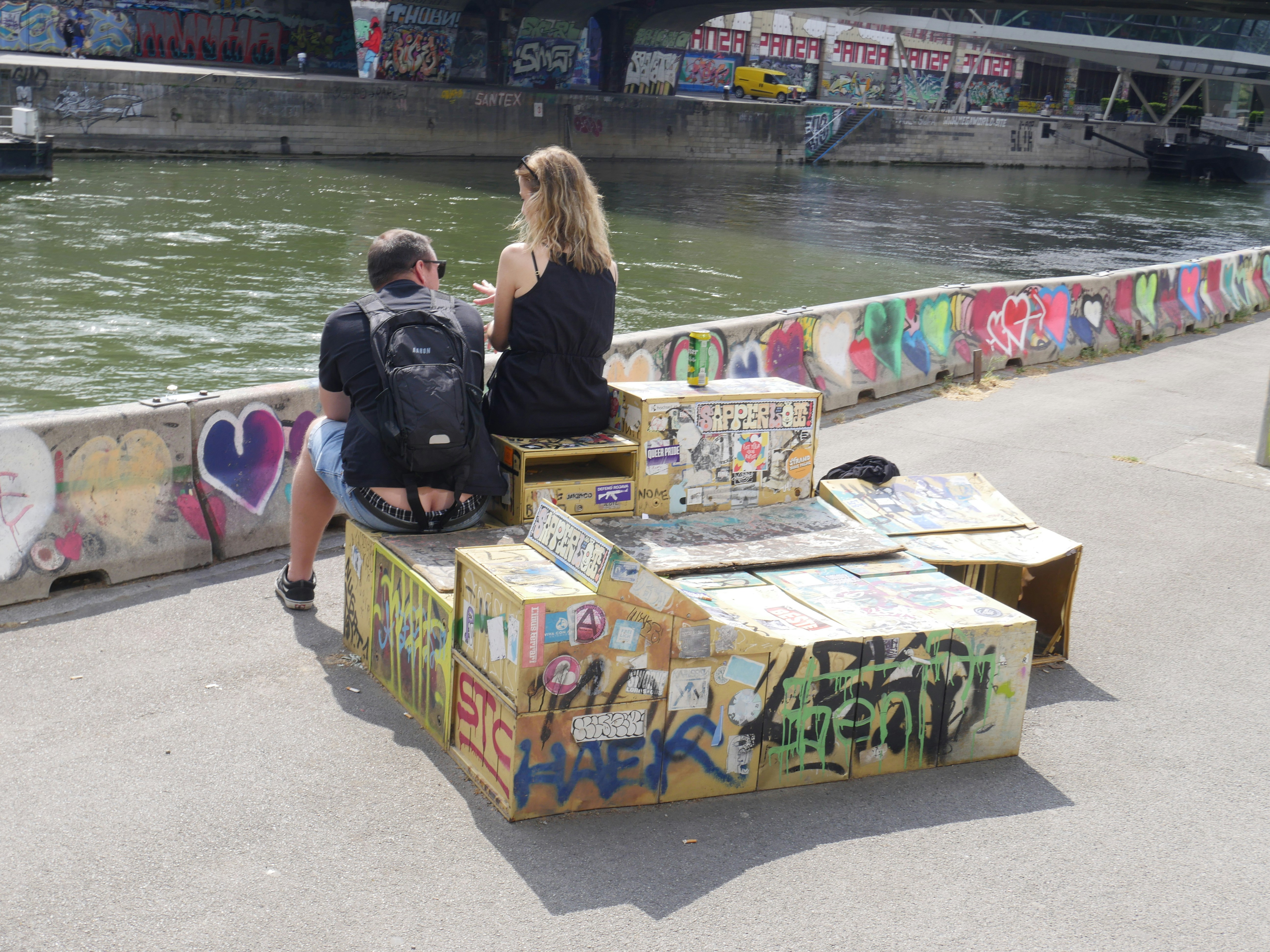 Graffiti Steps by the River: Two Friends Rest amid Painted Boxes