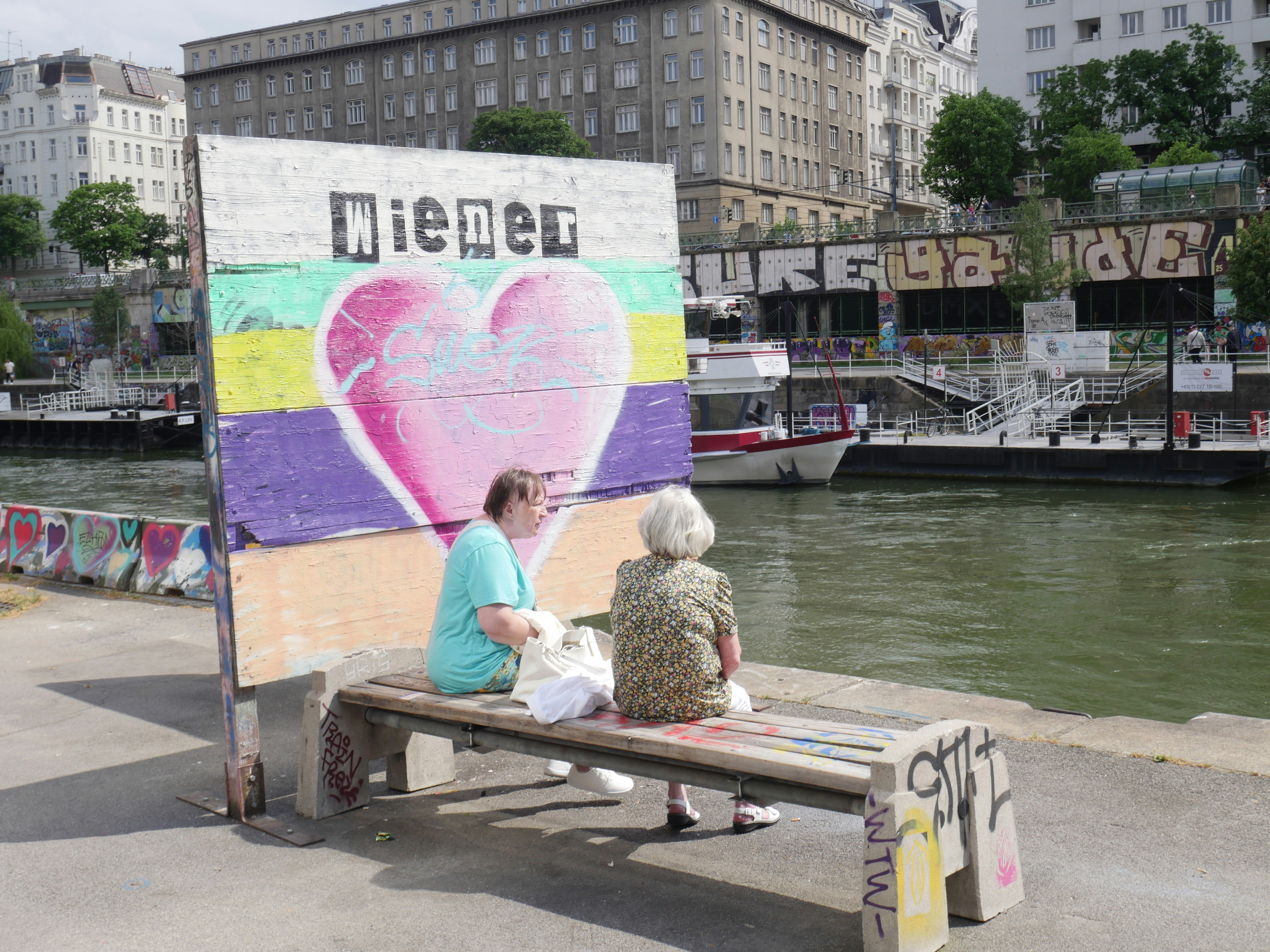 Heart mural by the river: two people sharing a quiet moment on a bench