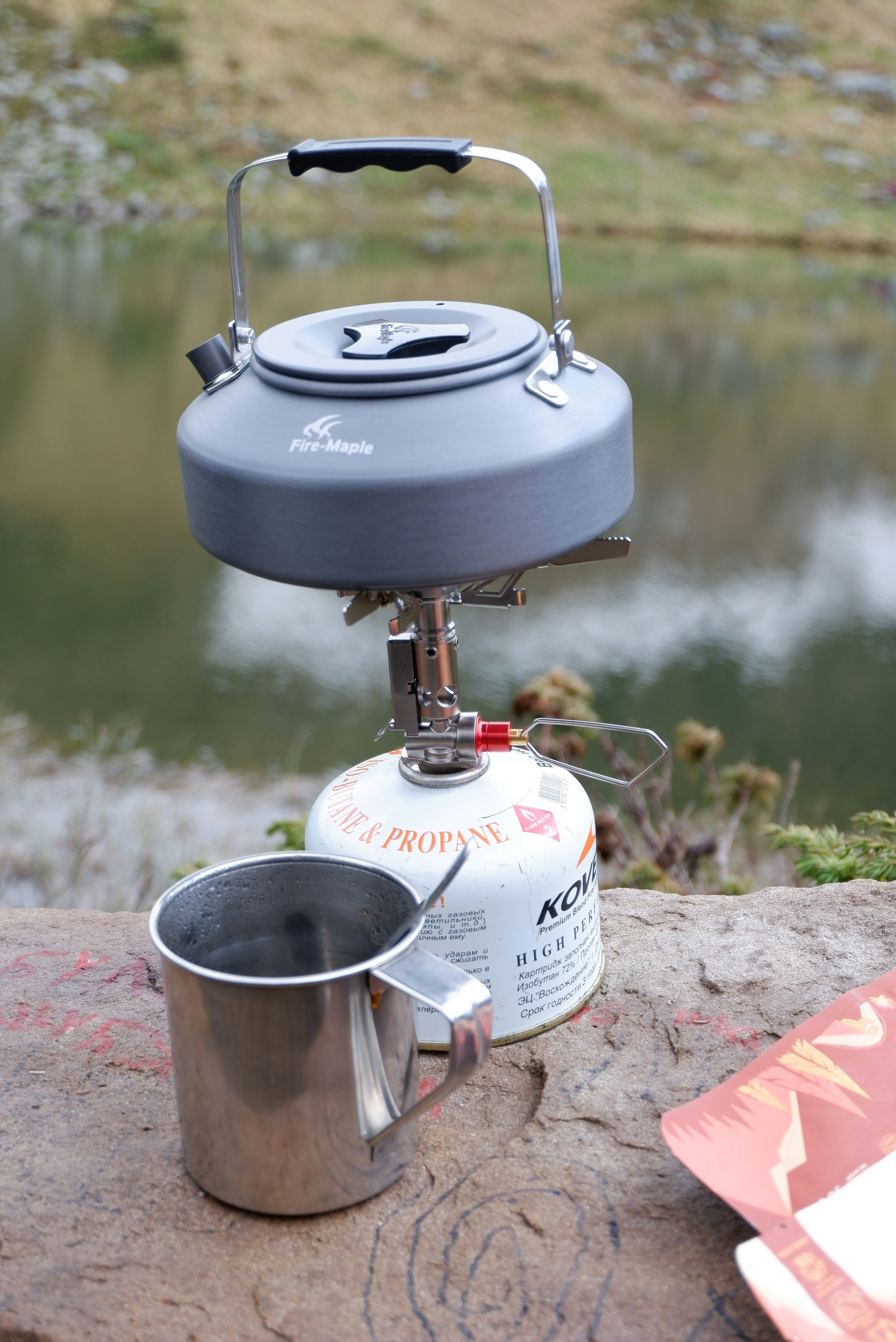 Campfire Kitchen on the Edge: A portable stove and kettle set against a tranquil lakeside.
