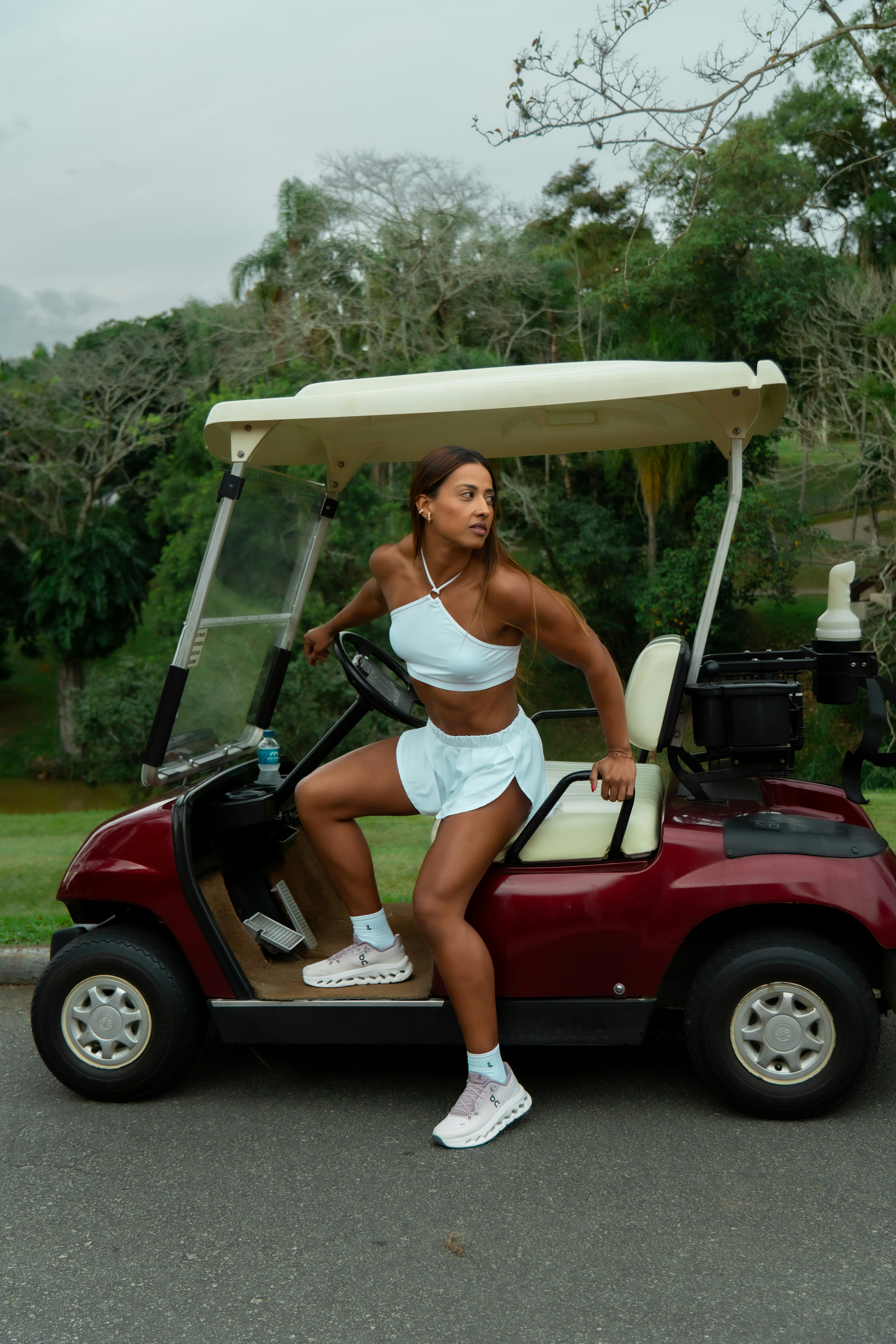 A woman in athletic wear exits a maroon golf cart.