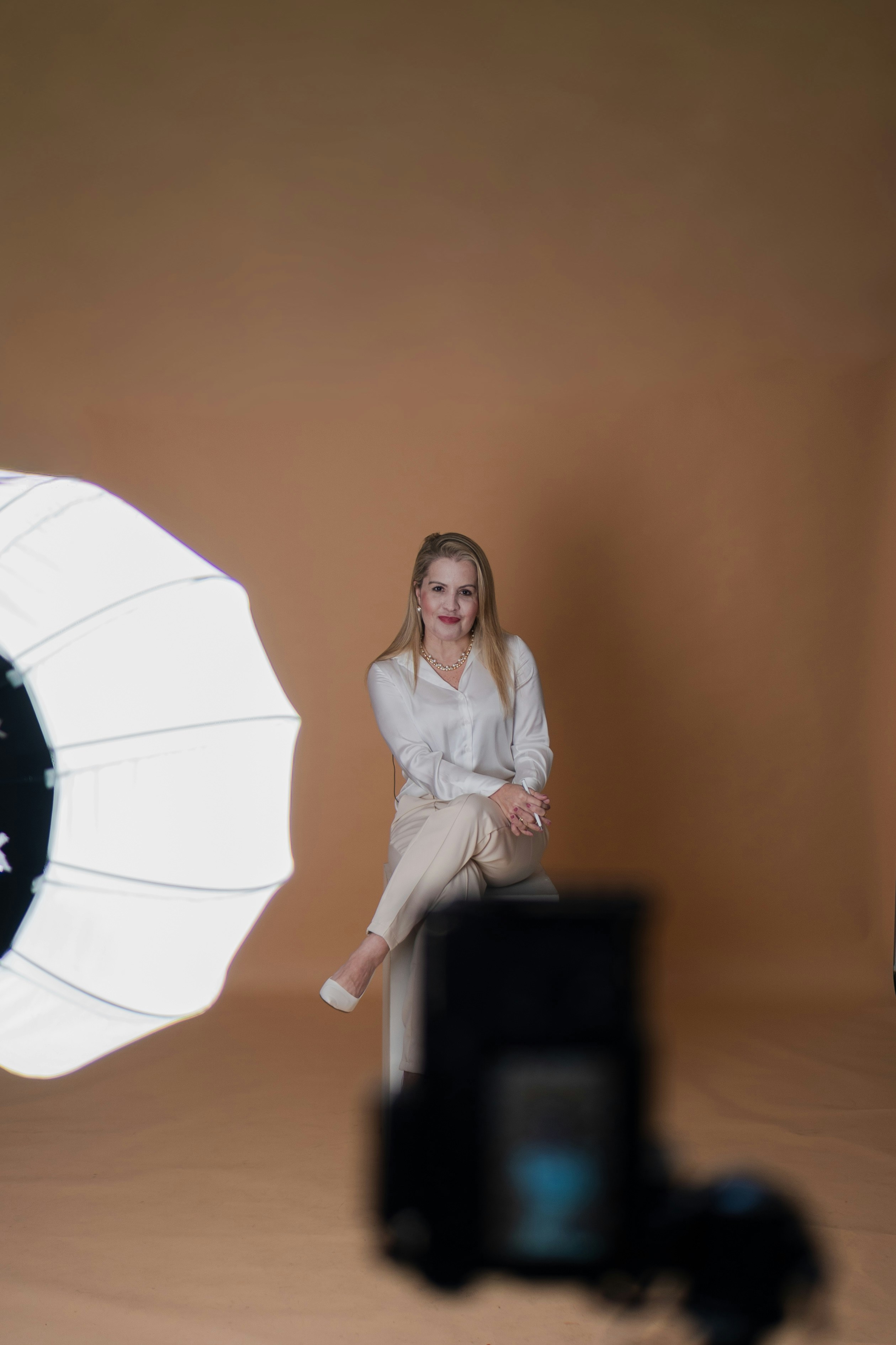 Softly lit studio portrait with a seated model in white against a warm backdrop