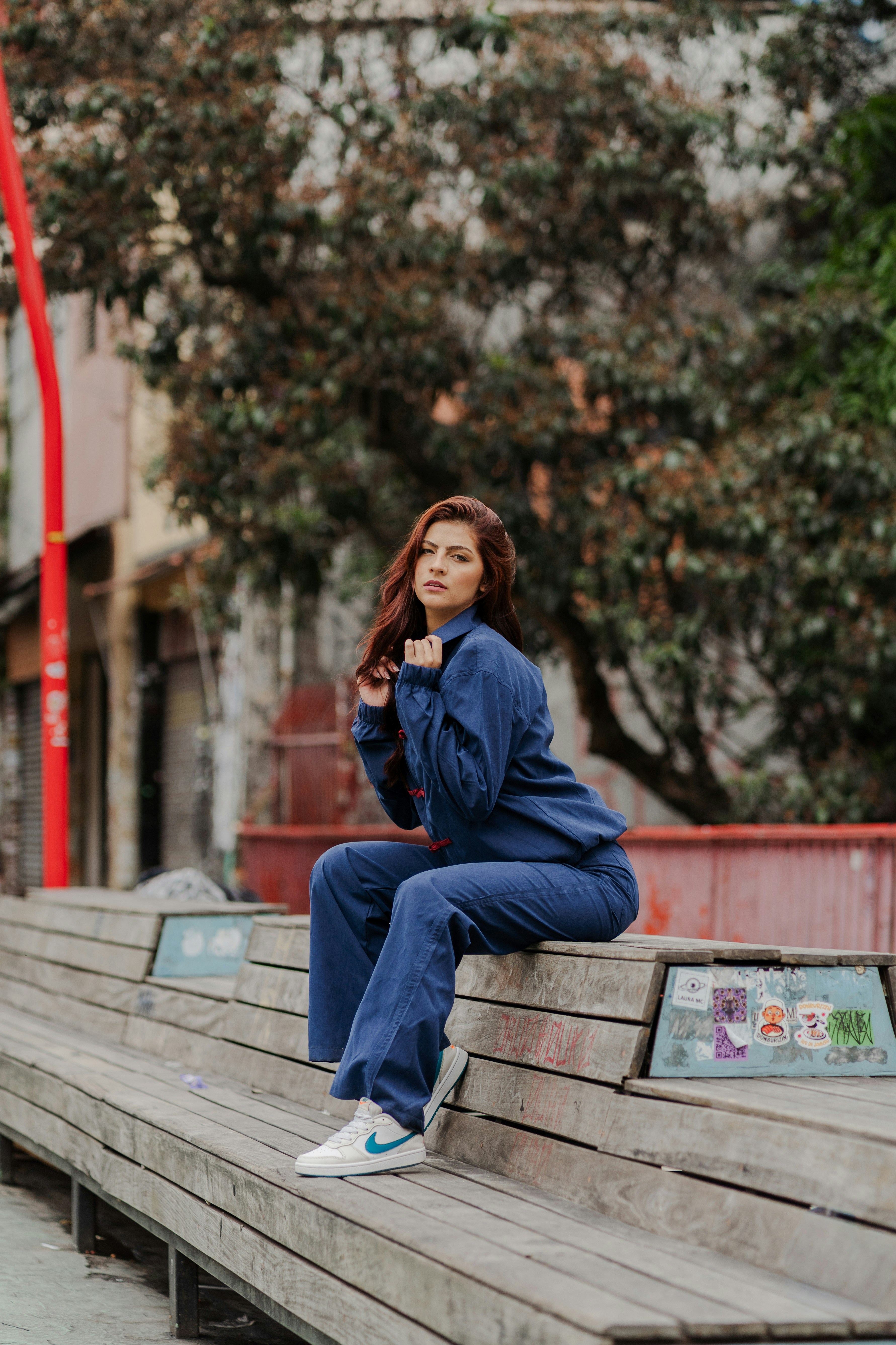 Red-haired woman in blue tracksuit sitting on urban wooden bench.