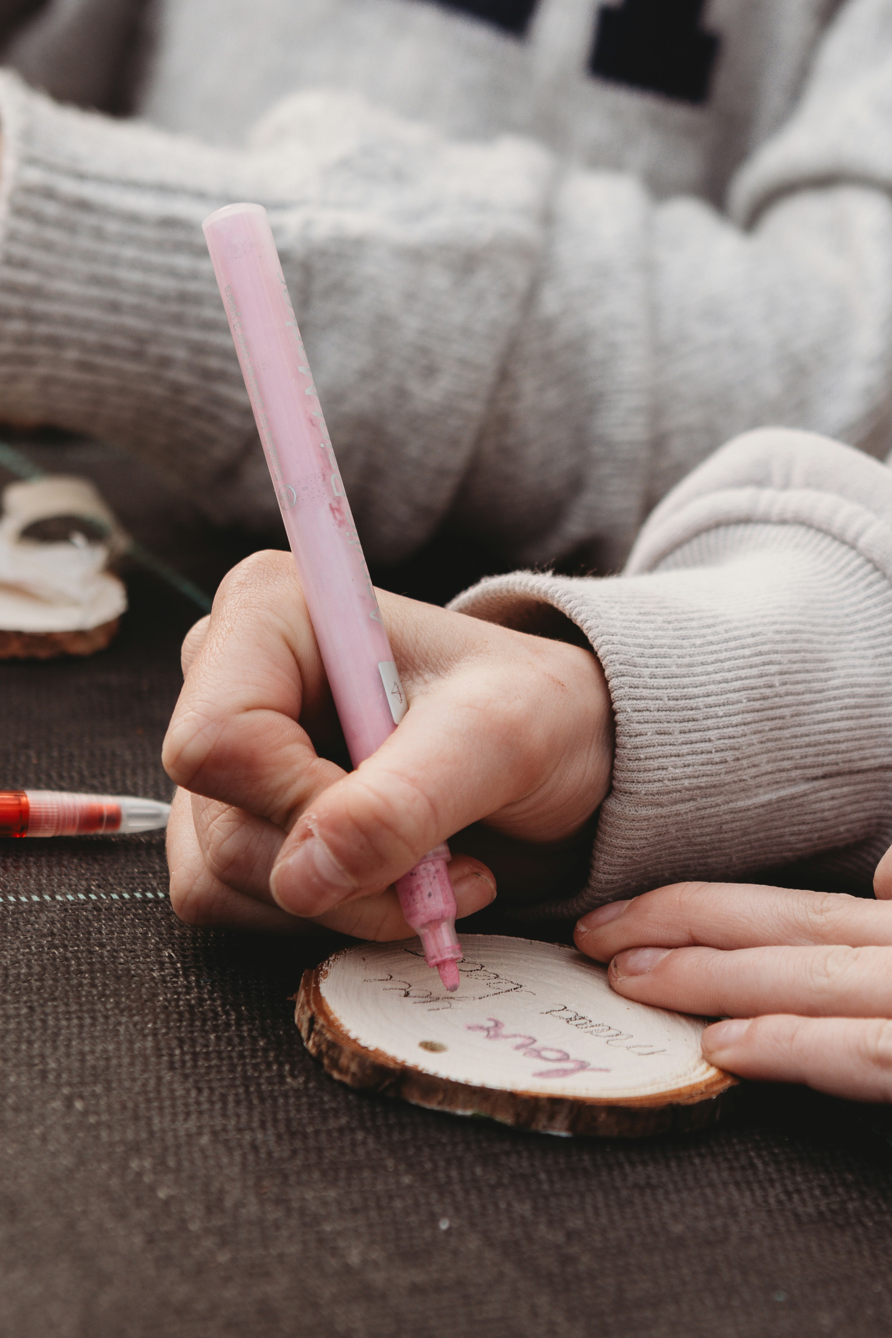 Pink Marker, Focused Hands: A Child Draws on a Wooden Slice
