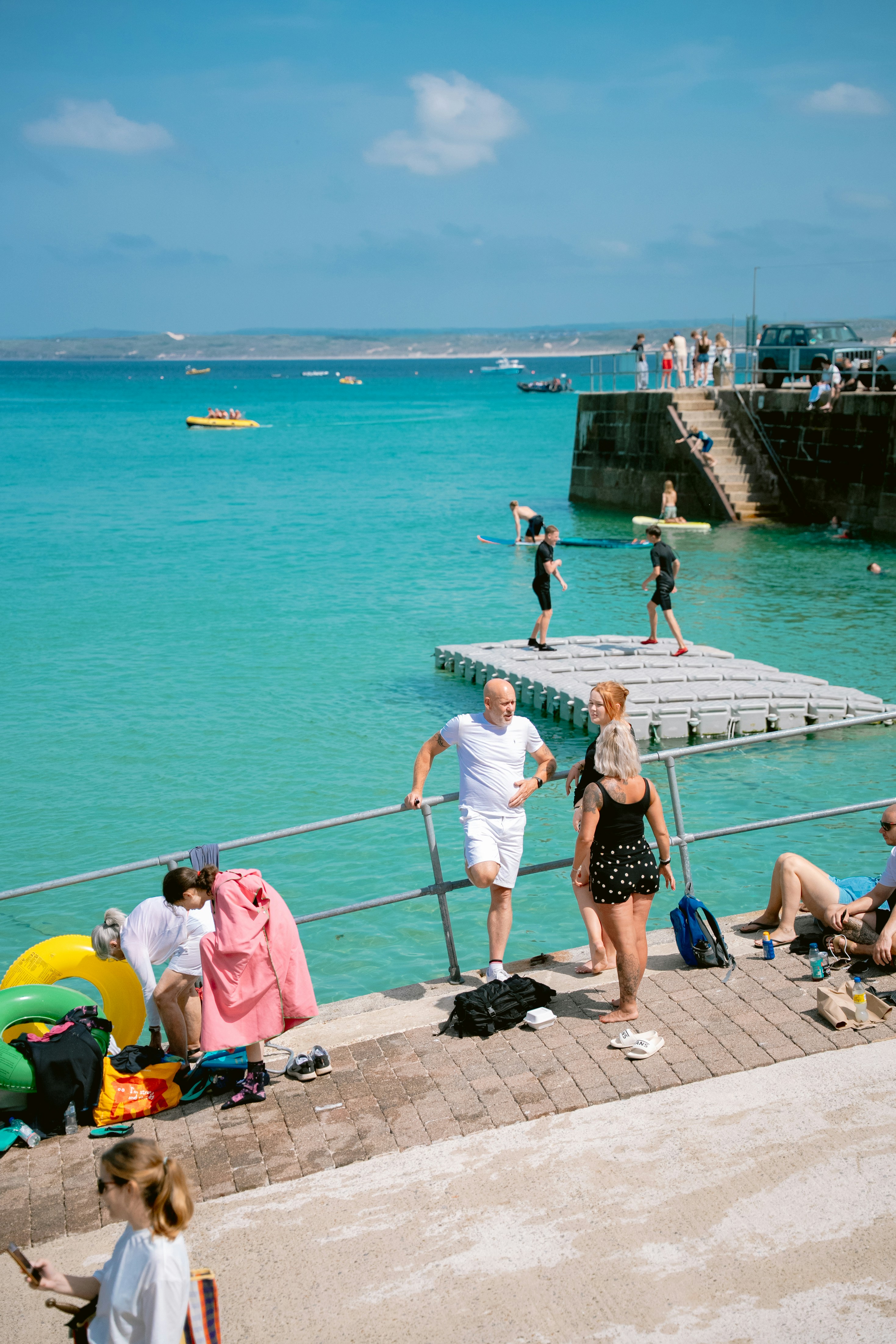 Sunlit Promenade: Coastline, Swimmers, and Social Pause
