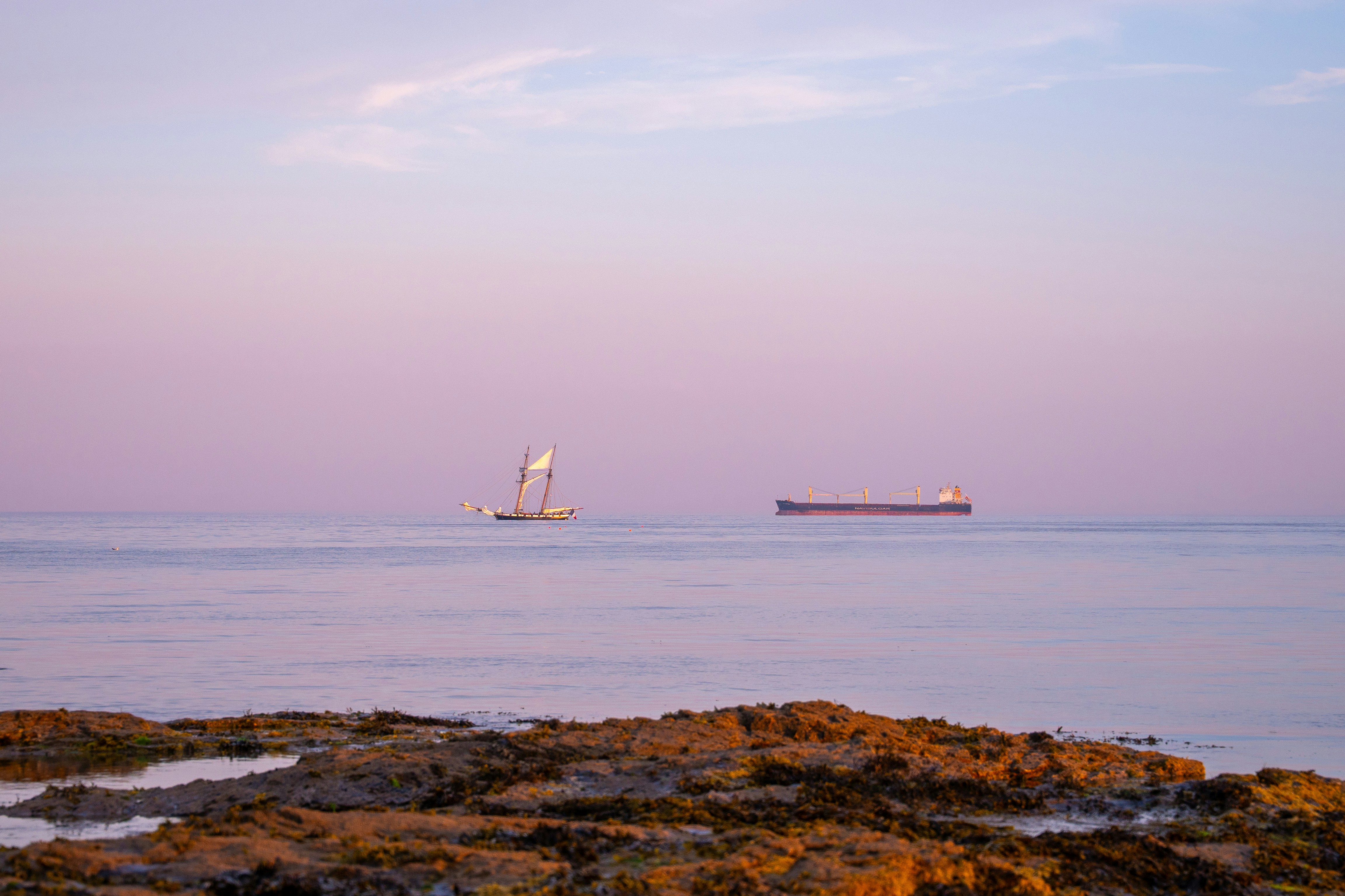 Calm Sea Tranquility: Sailboat and Cargo Ship on a Sunset Hour