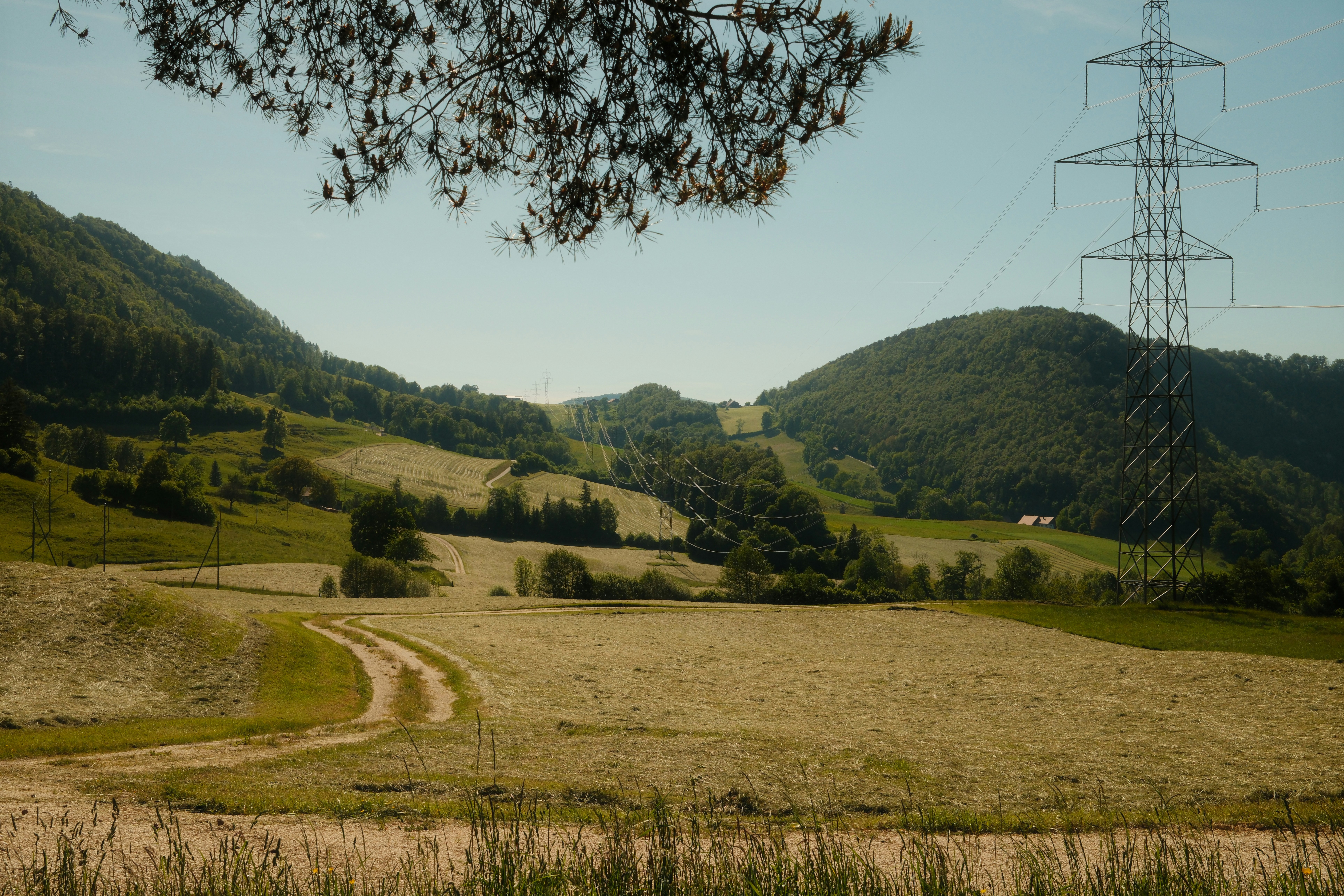 Dirt road through fields, green hills, and a power pylon.