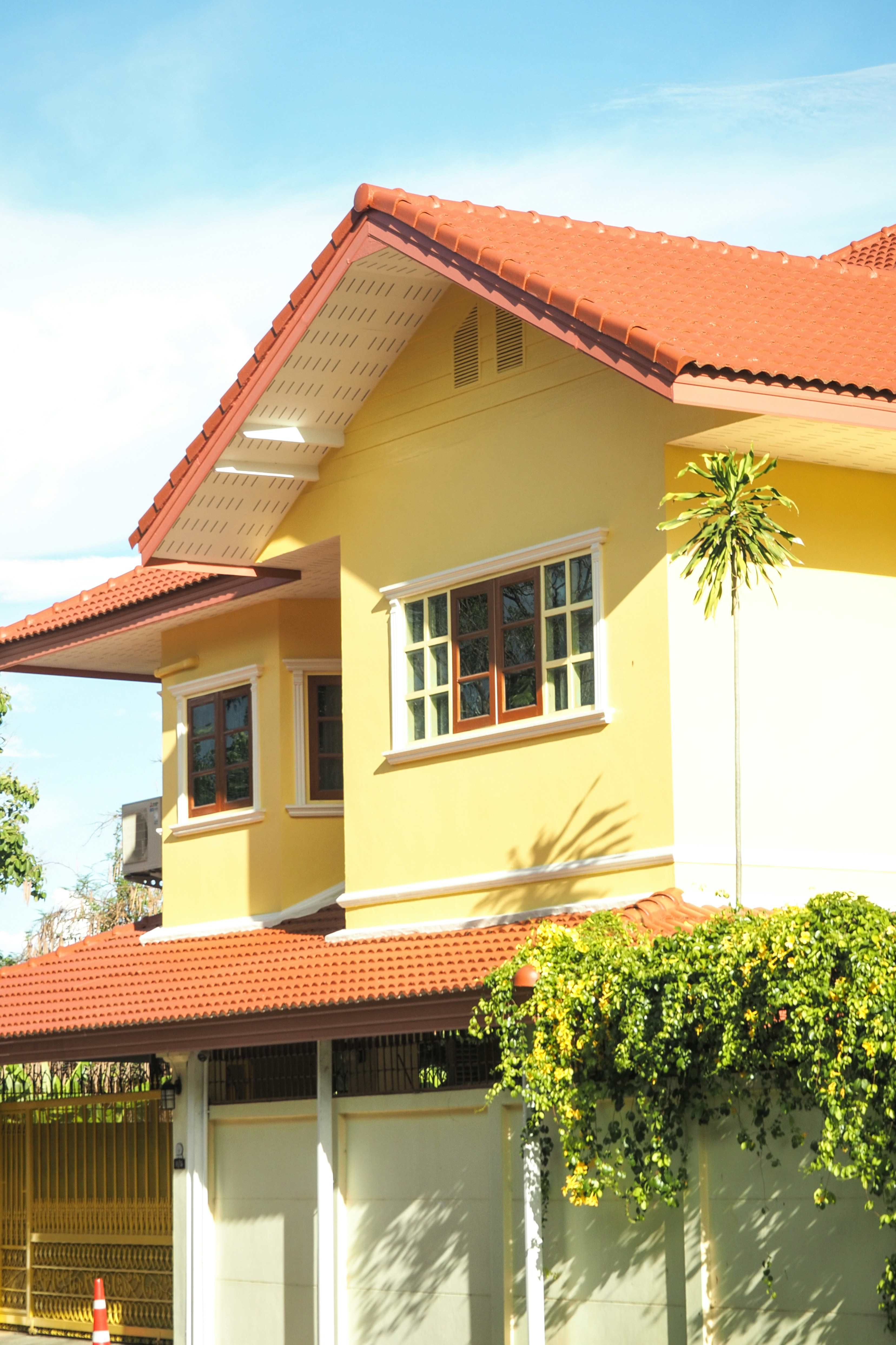 A yellow house with a red roof and green vines.