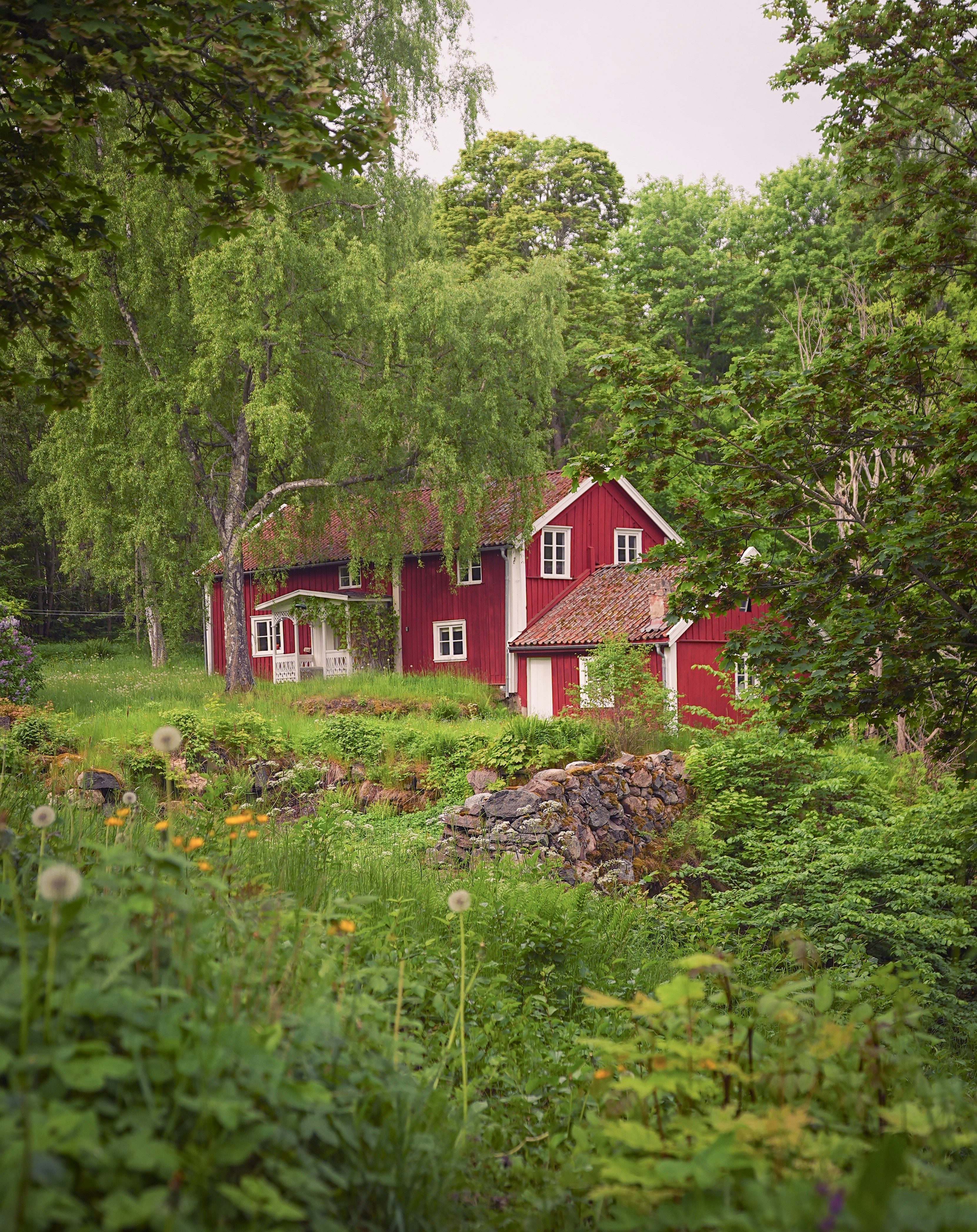 A red house nestled among green trees and wildflowers.