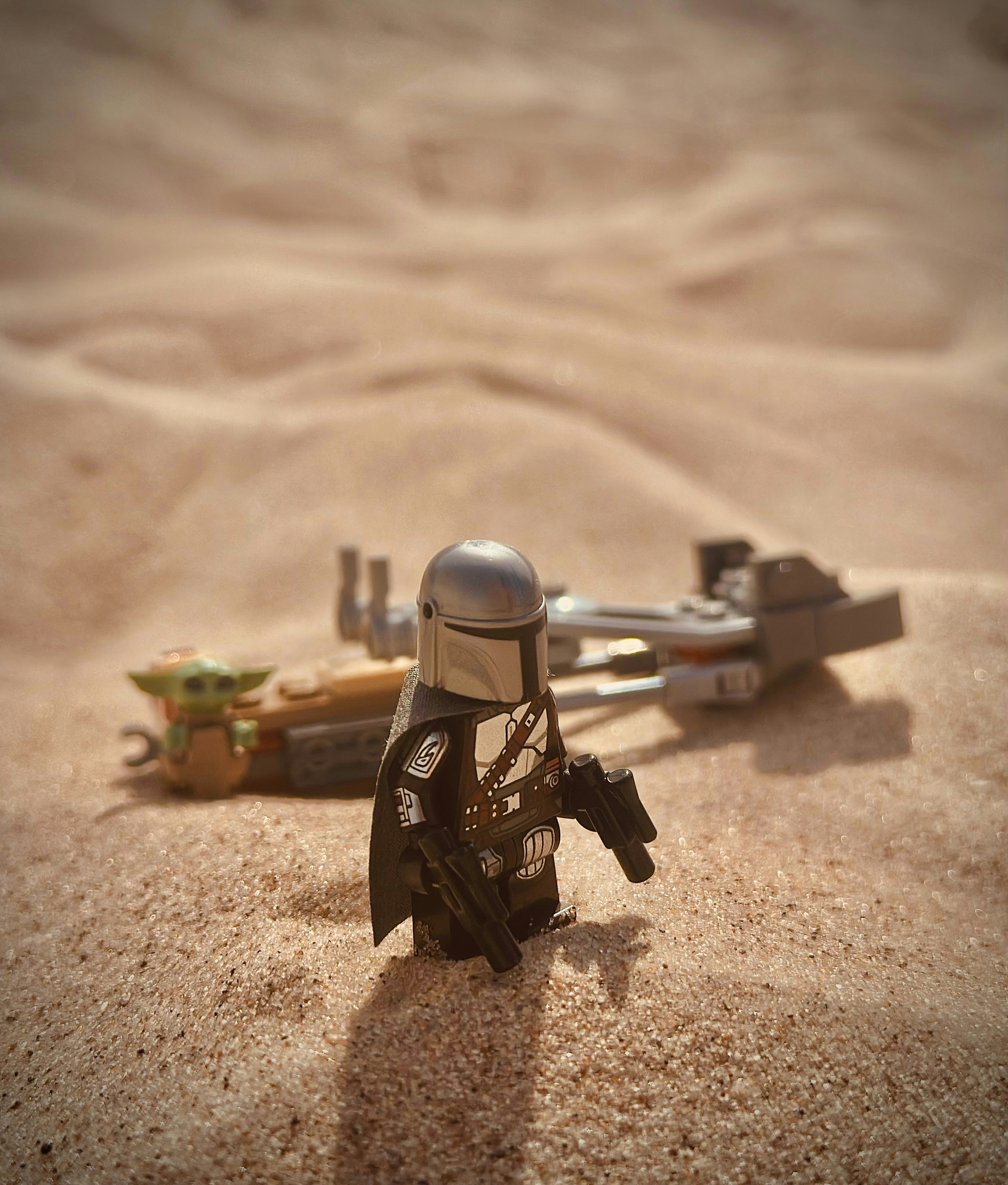 Lego mandalorian minifigure with blasters on a sandy desert.