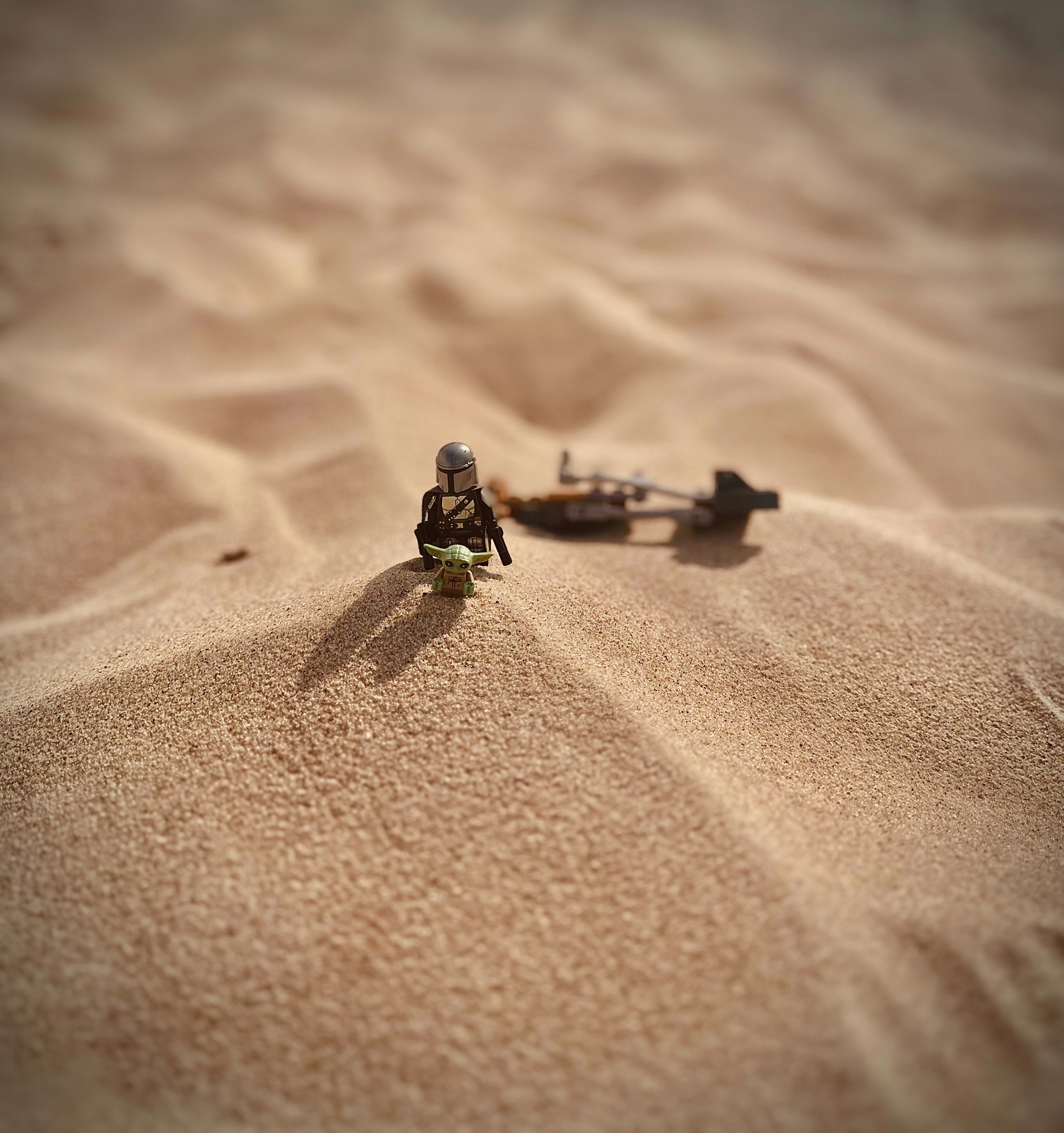 Mandalorian toy figure stands in desert sand.