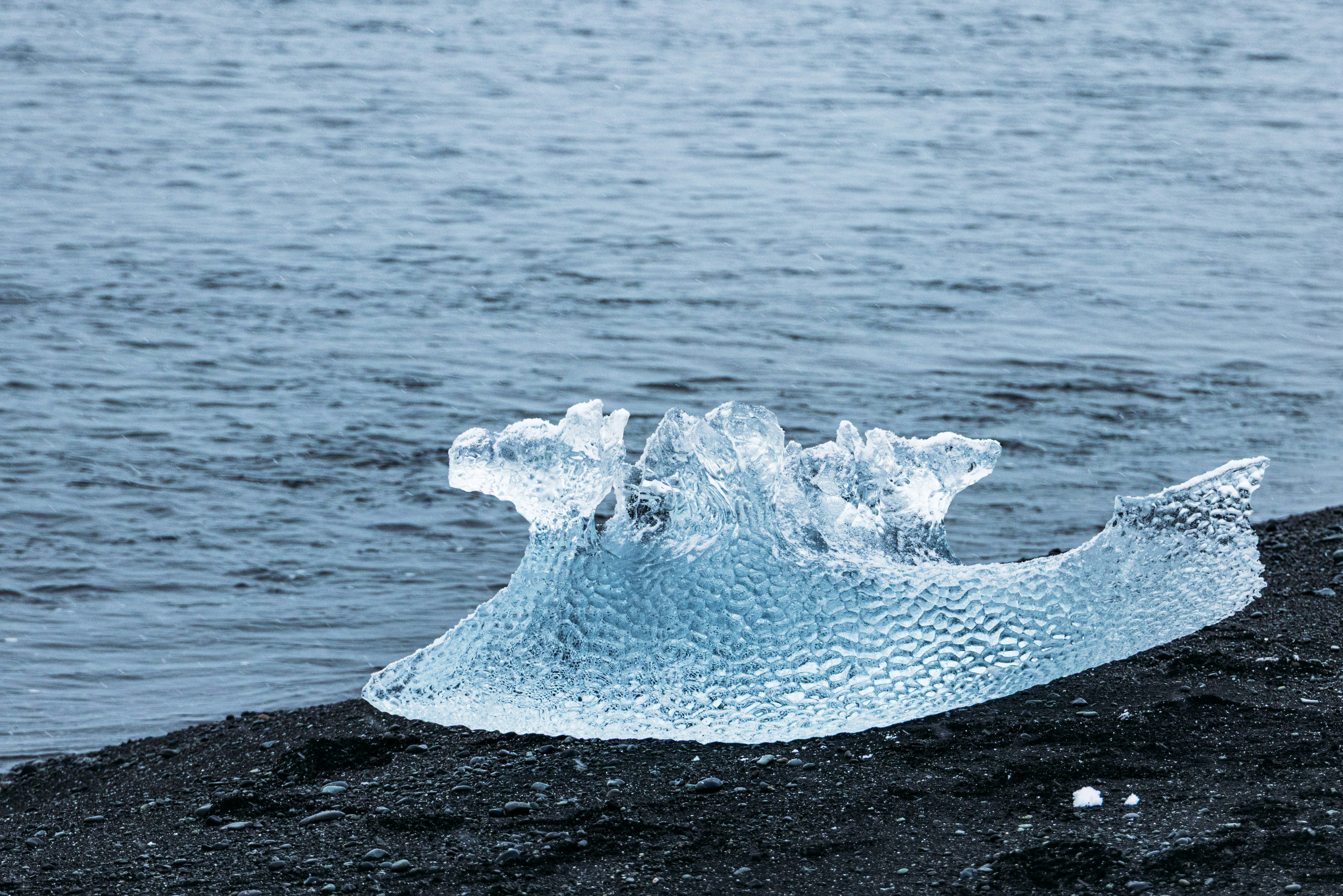 Ice Sculpted Edge: a lone iceberg resting on volcanic pebble shore