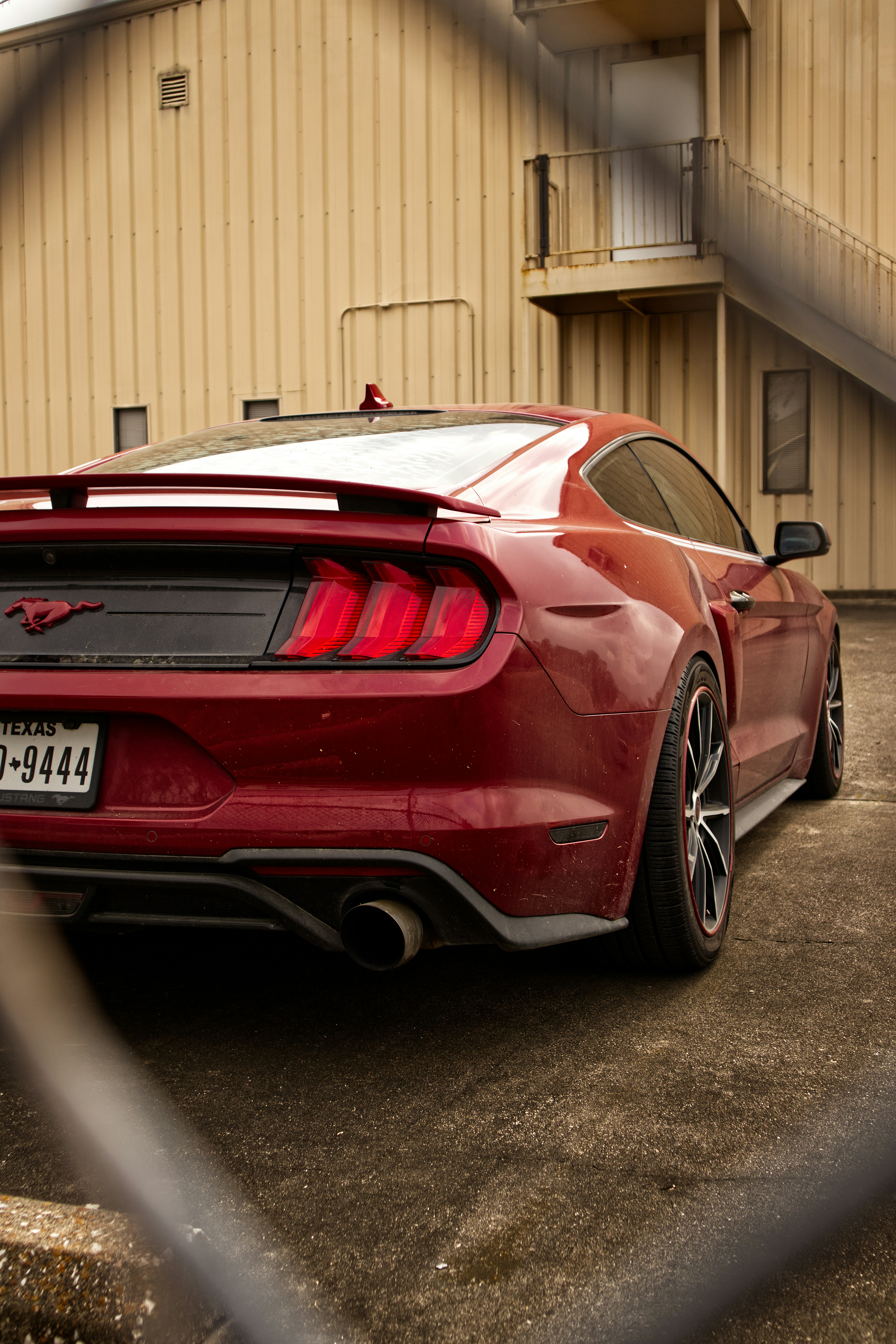 Red Mustang at Rest: A Close-Up of Powerful Curves by an Industrial Facade