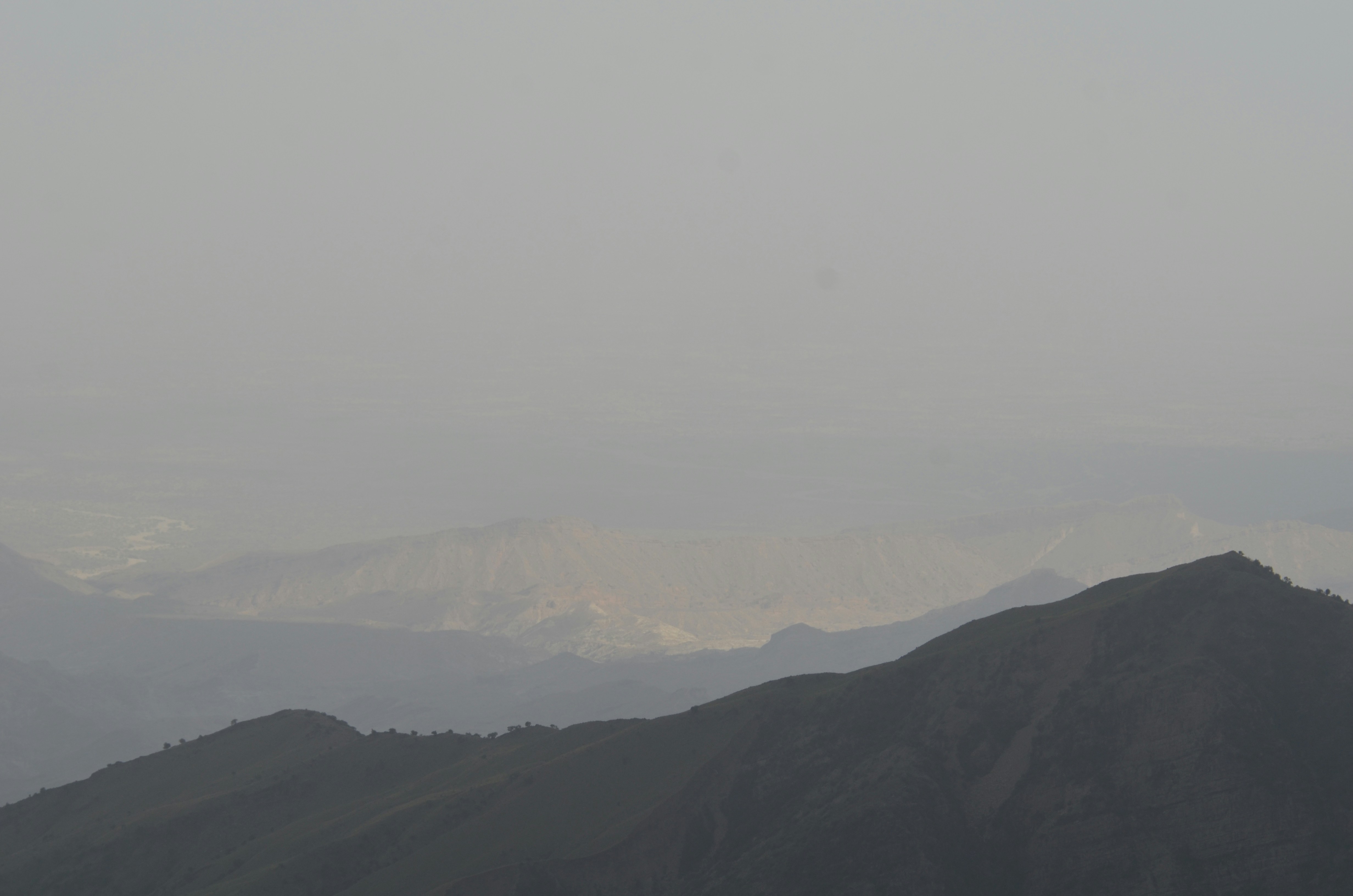 Hazy mountain ridge and distant valleys stretch across the horizon, with a dark fore­ground ridge in the lower portion of the frame.