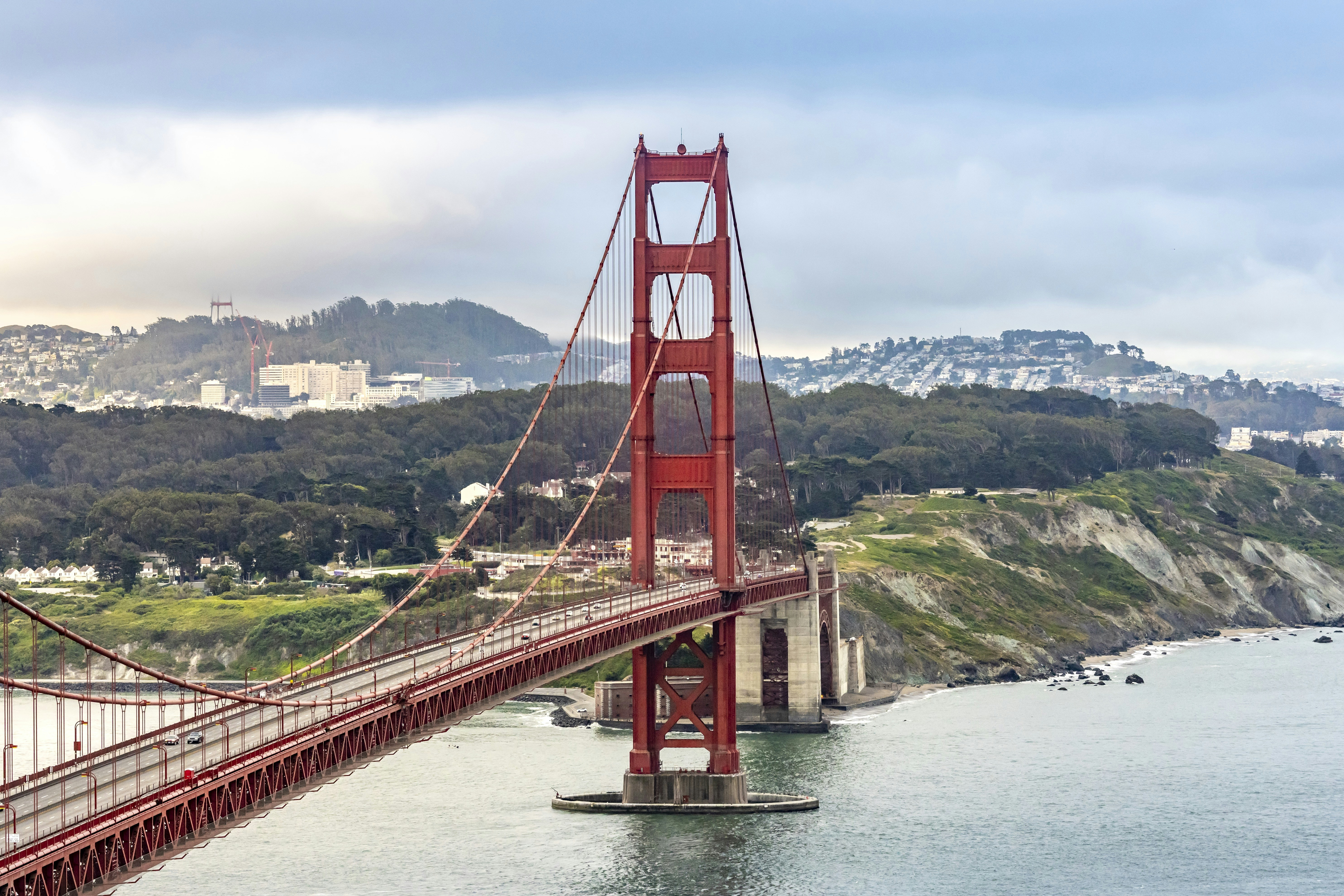 Golden gate bridge spans across water with distant hills.