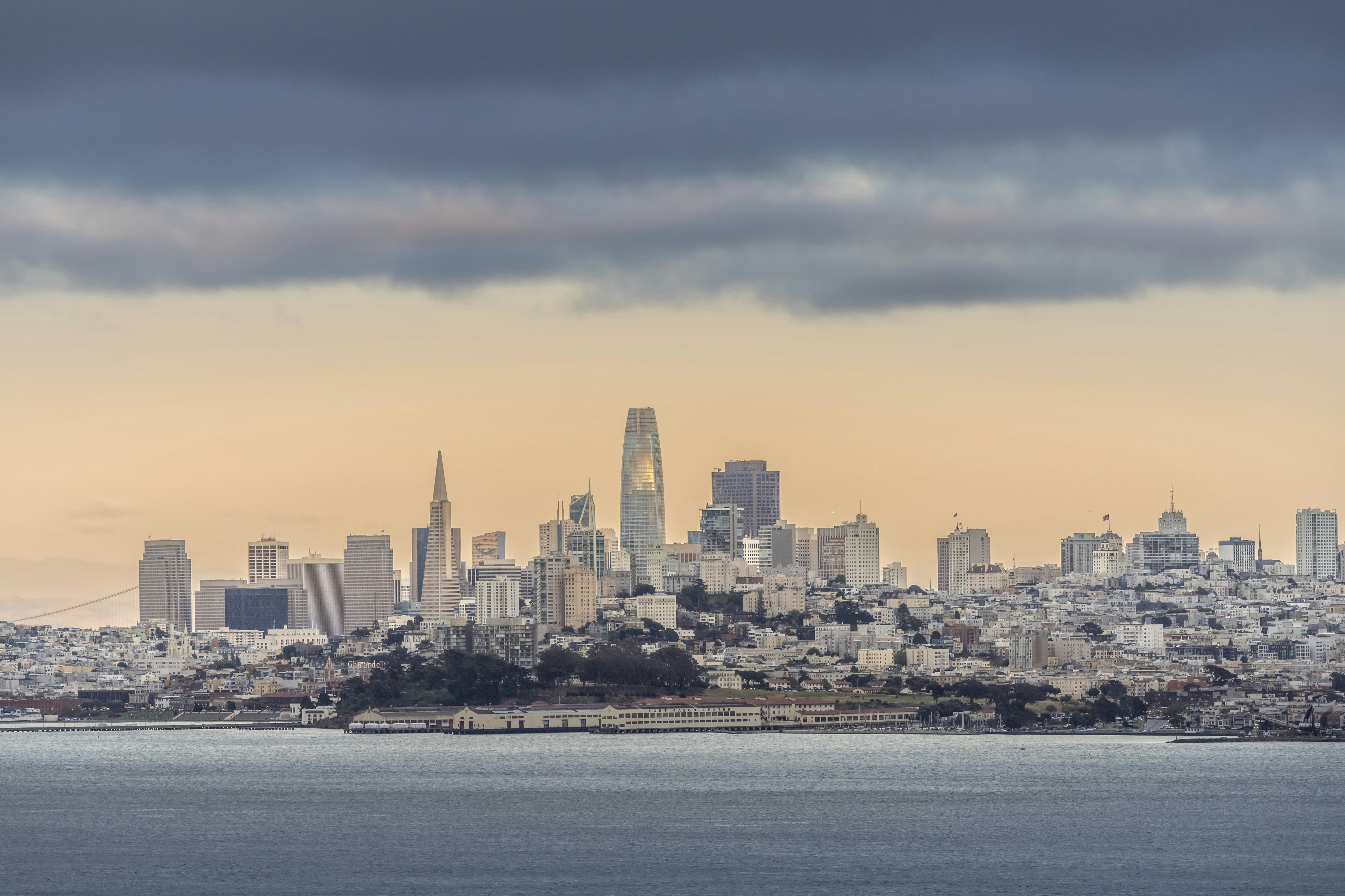 San francisco cityscape with skyscrapers, water, and cloudy sky.