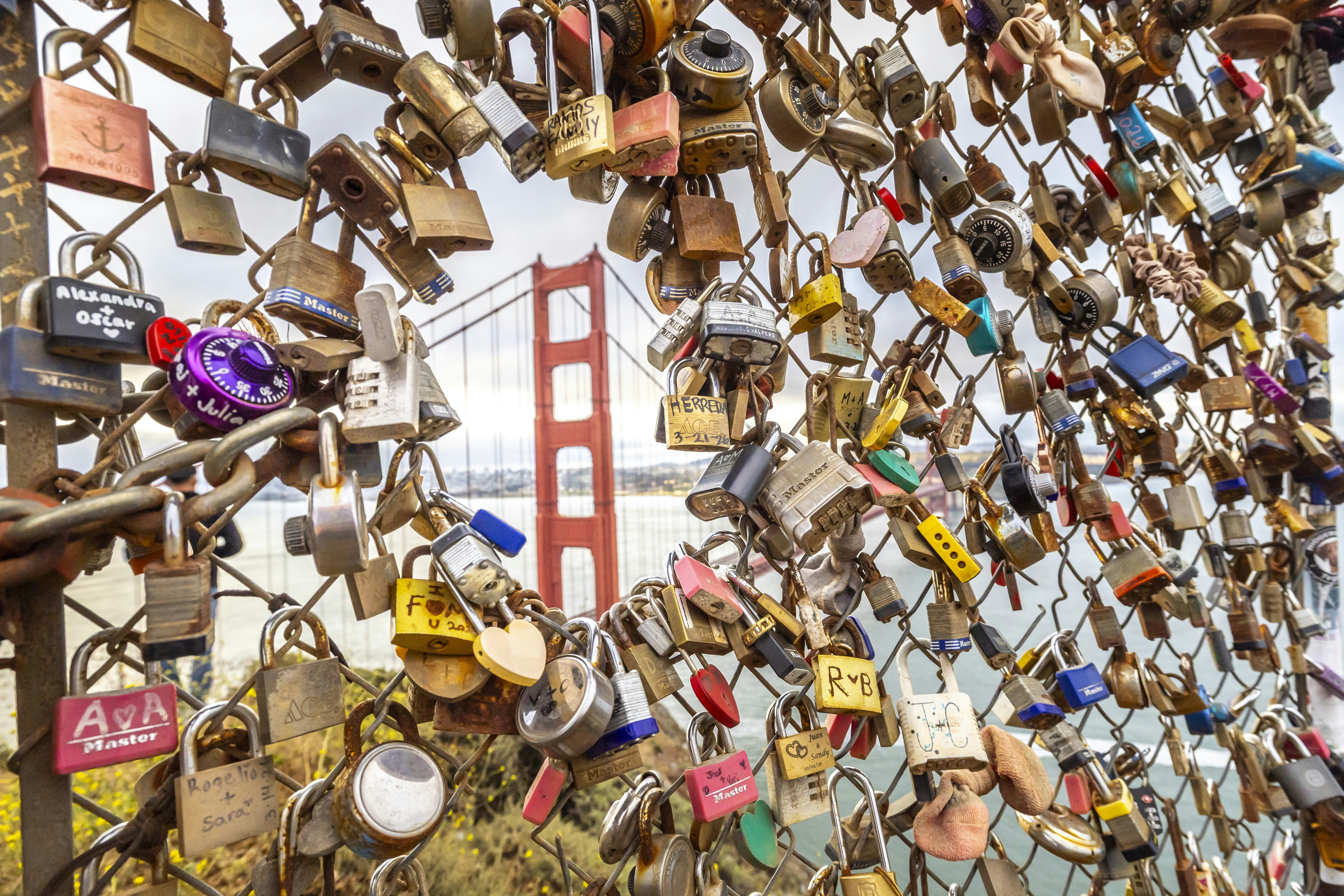 Colorful padlocks on a fence, with the golden gate bridge.
