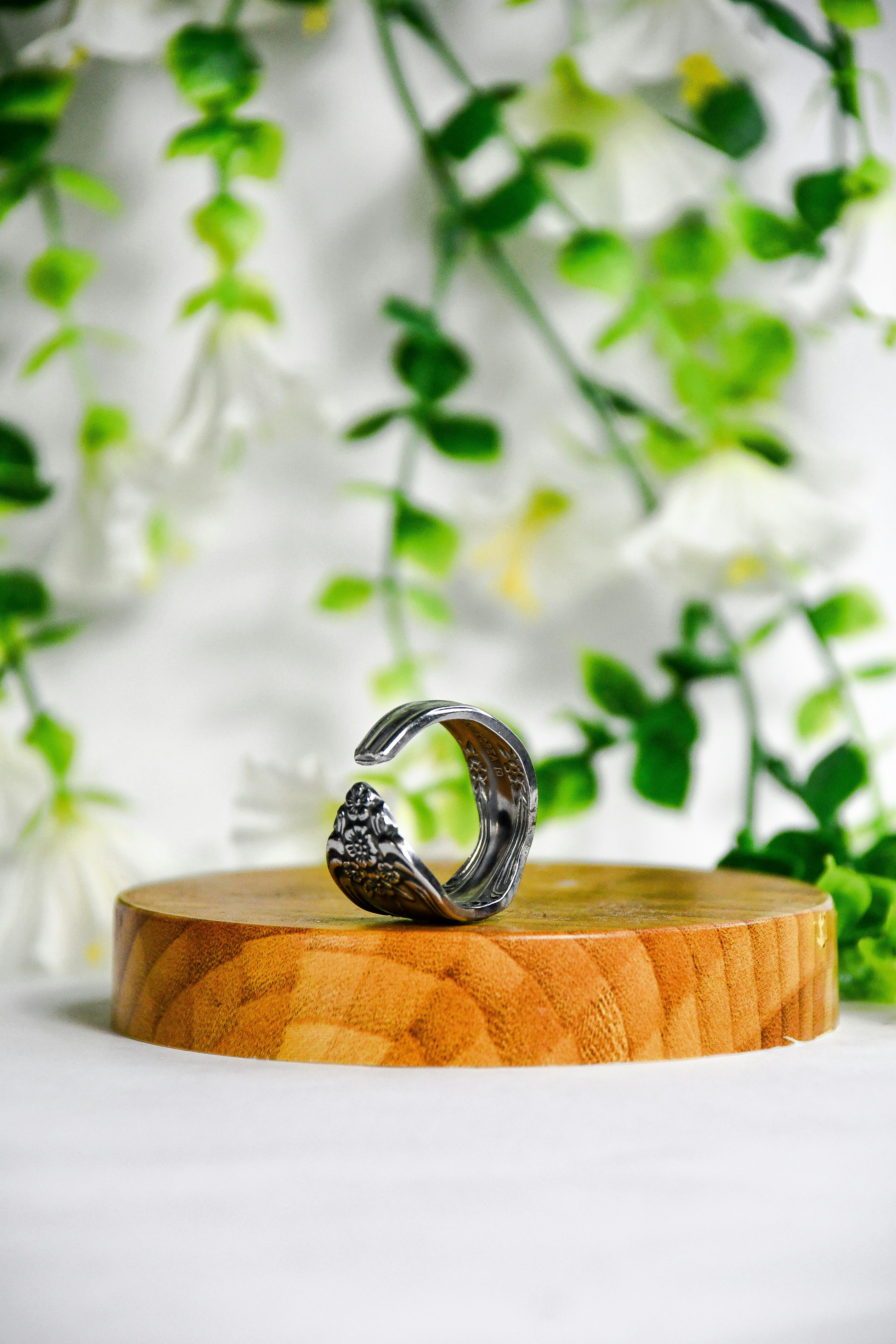 Elegant ring perched on a wooden pedestal with cascading greenery backdrop