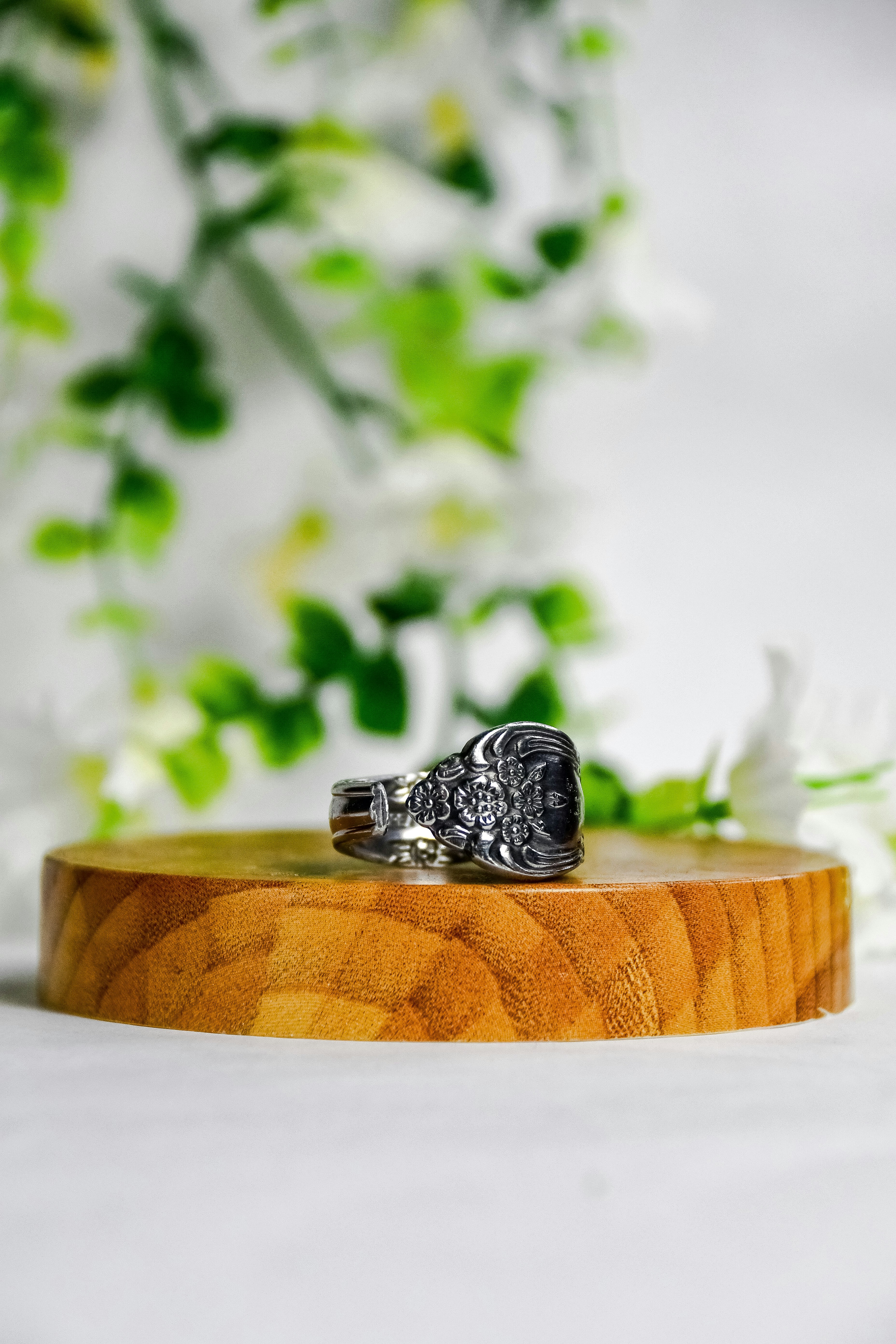Ornate Ring on a Wooden Pedestal Under Soft Greenery