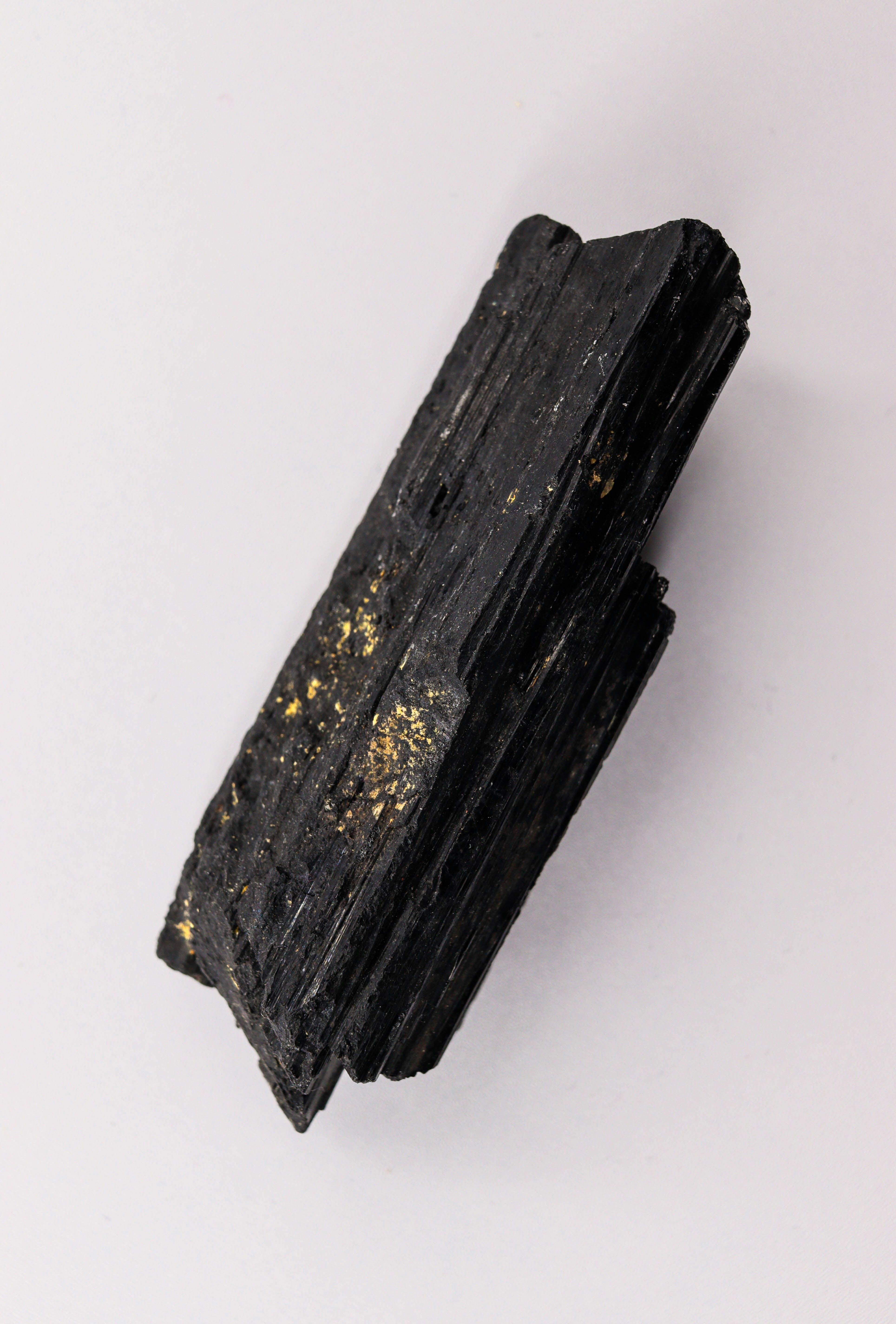 Black tourmaline crystal with golden specks on white background.