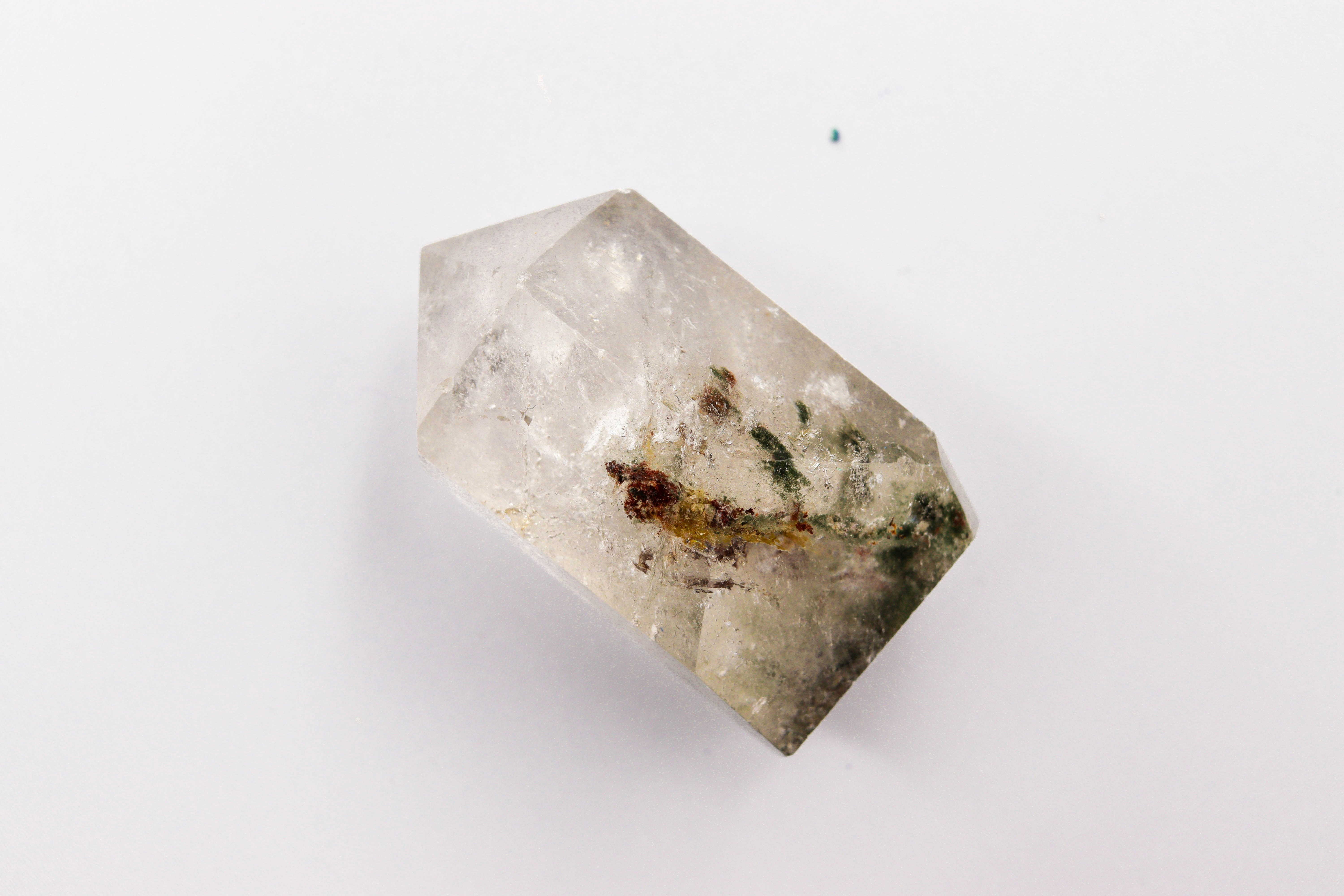 Clear quartz crystal point with green and brown inclusions.
