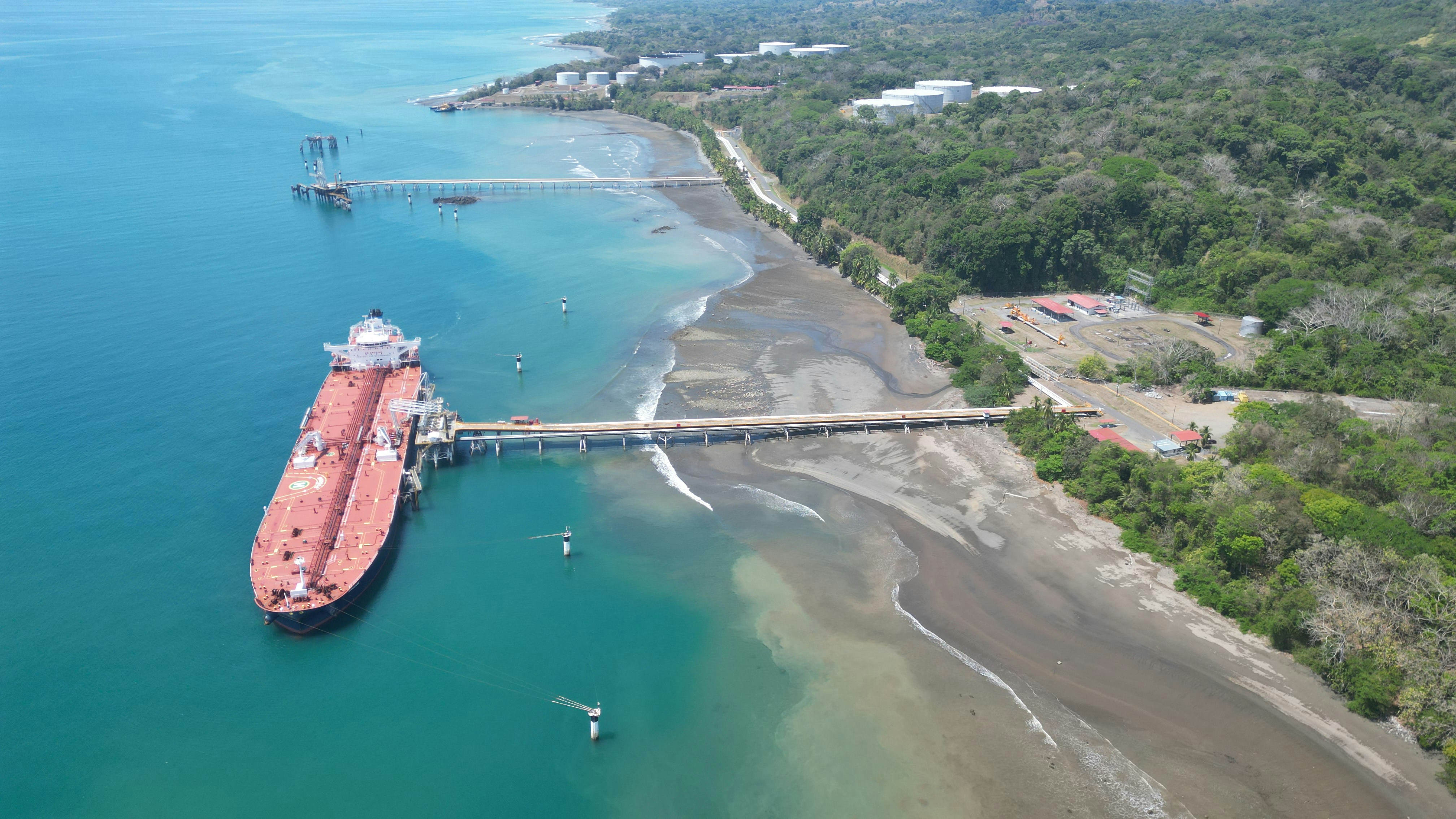 Red ship docked at a pier along a wooded coastline.