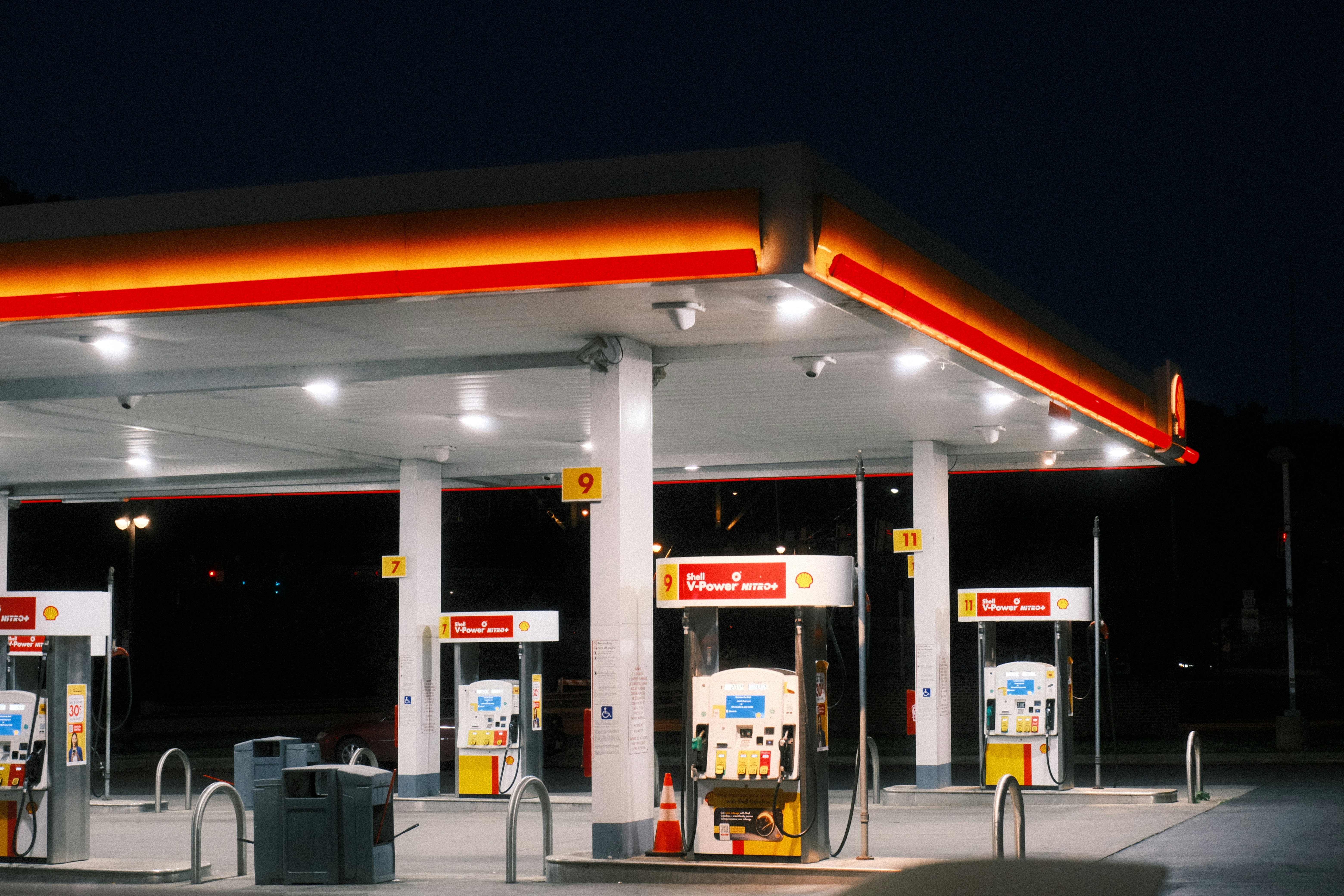 Illuminated gas station pumps under a bright canopy at night.