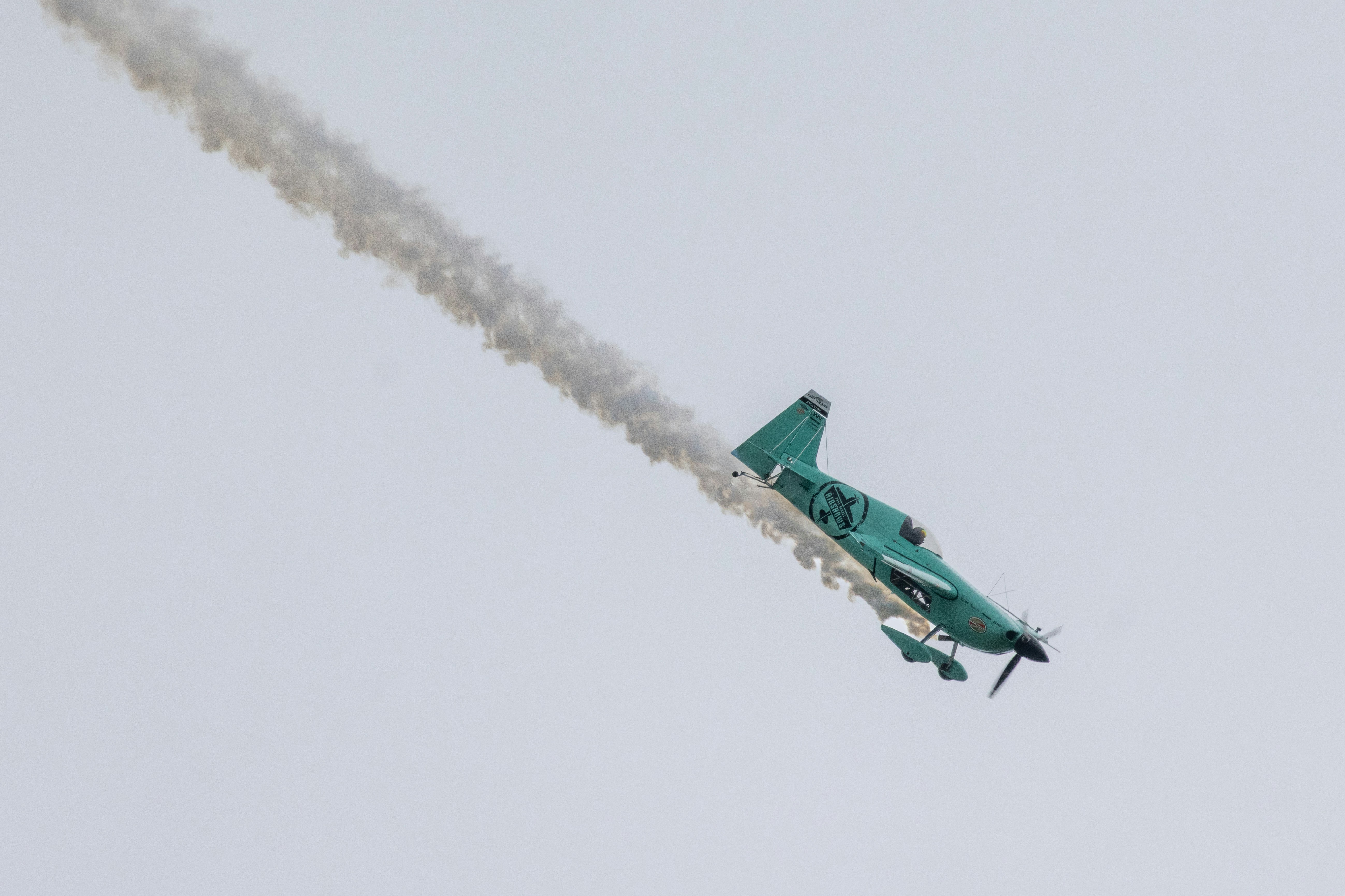 Teal Airshow Streak: A high-contrast moment of a smoke-trailing aerobatic plane