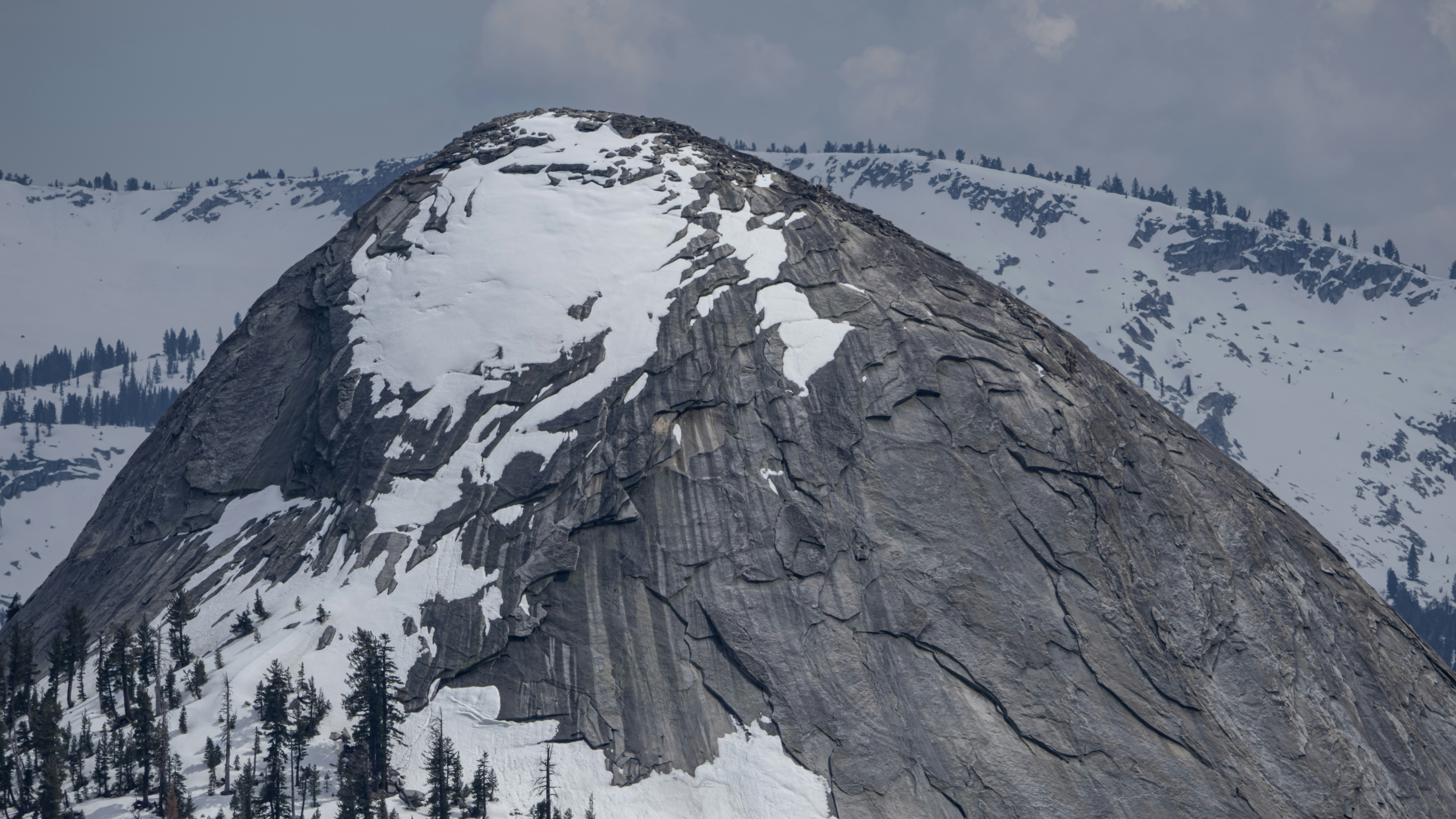 A large, snow-capped granite mountain peak with trees.