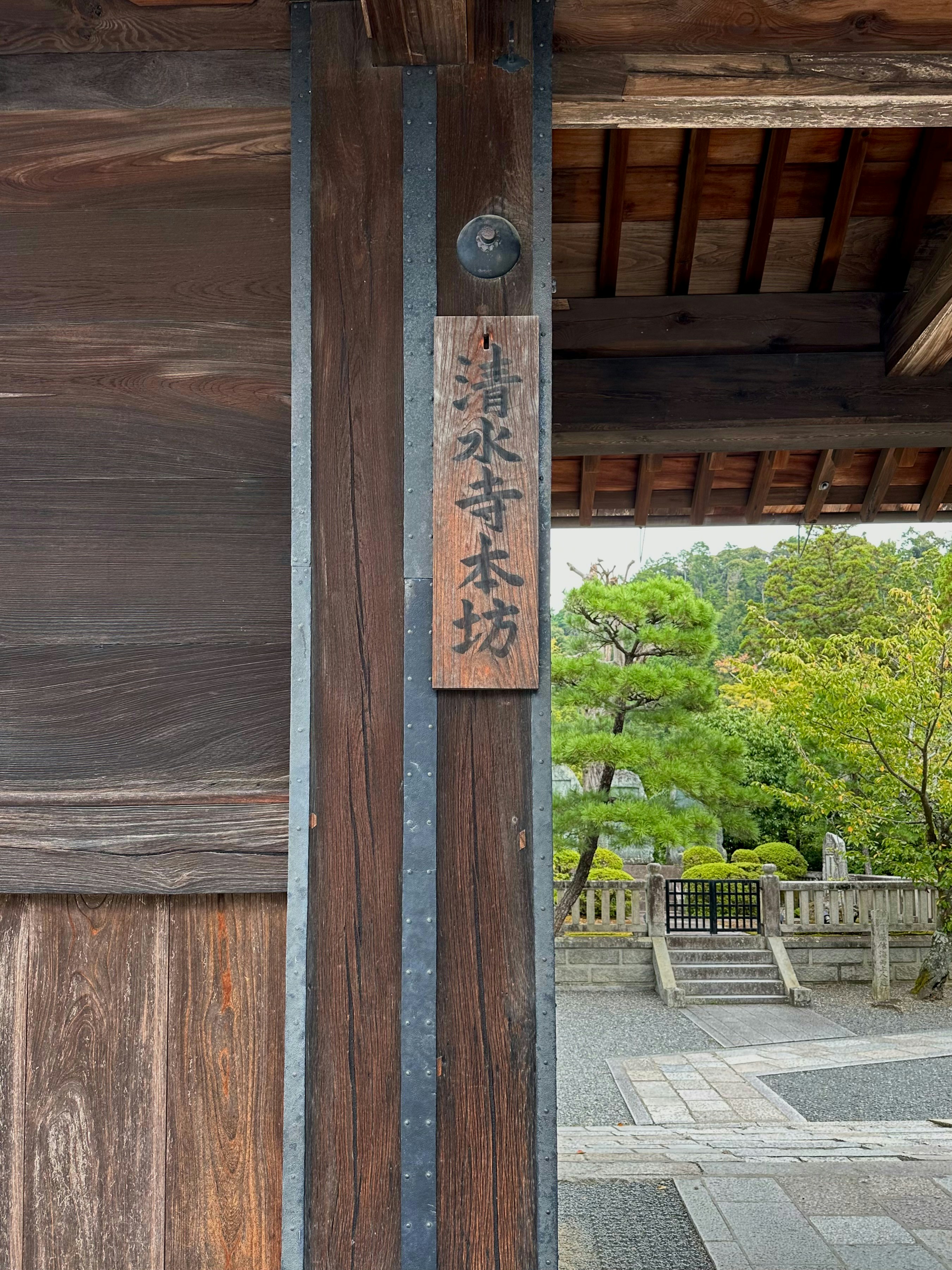 Japanese temple gate with a wooden sign and lush garden.