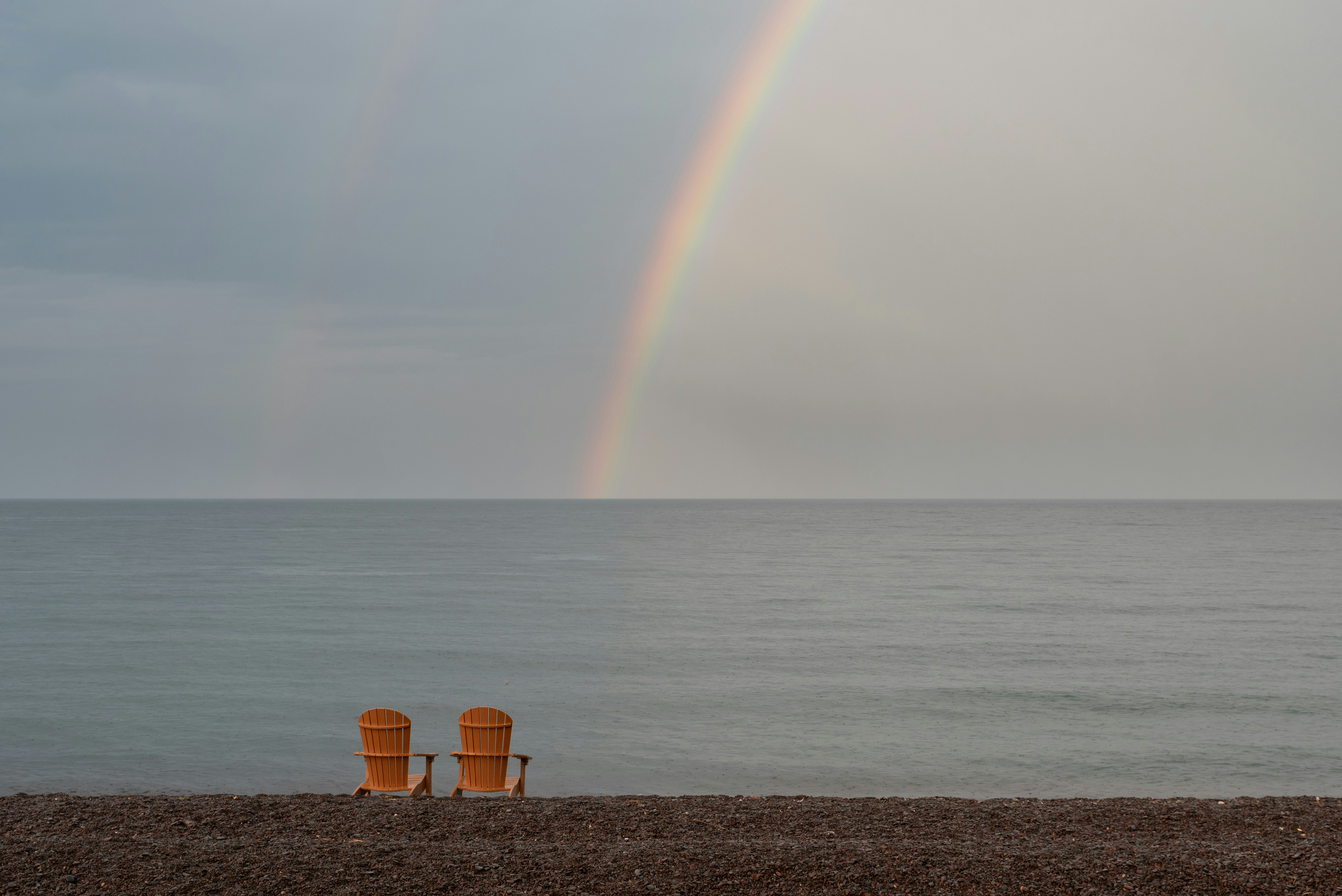 Twin Chairs Beneath a Rainbow Over Calm Seas