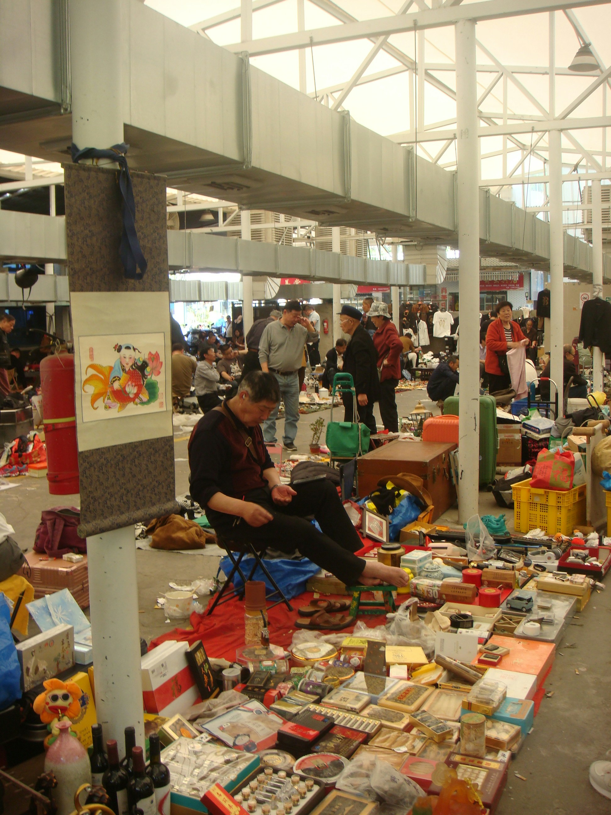 A busy outdoor market with people browsing various goods.