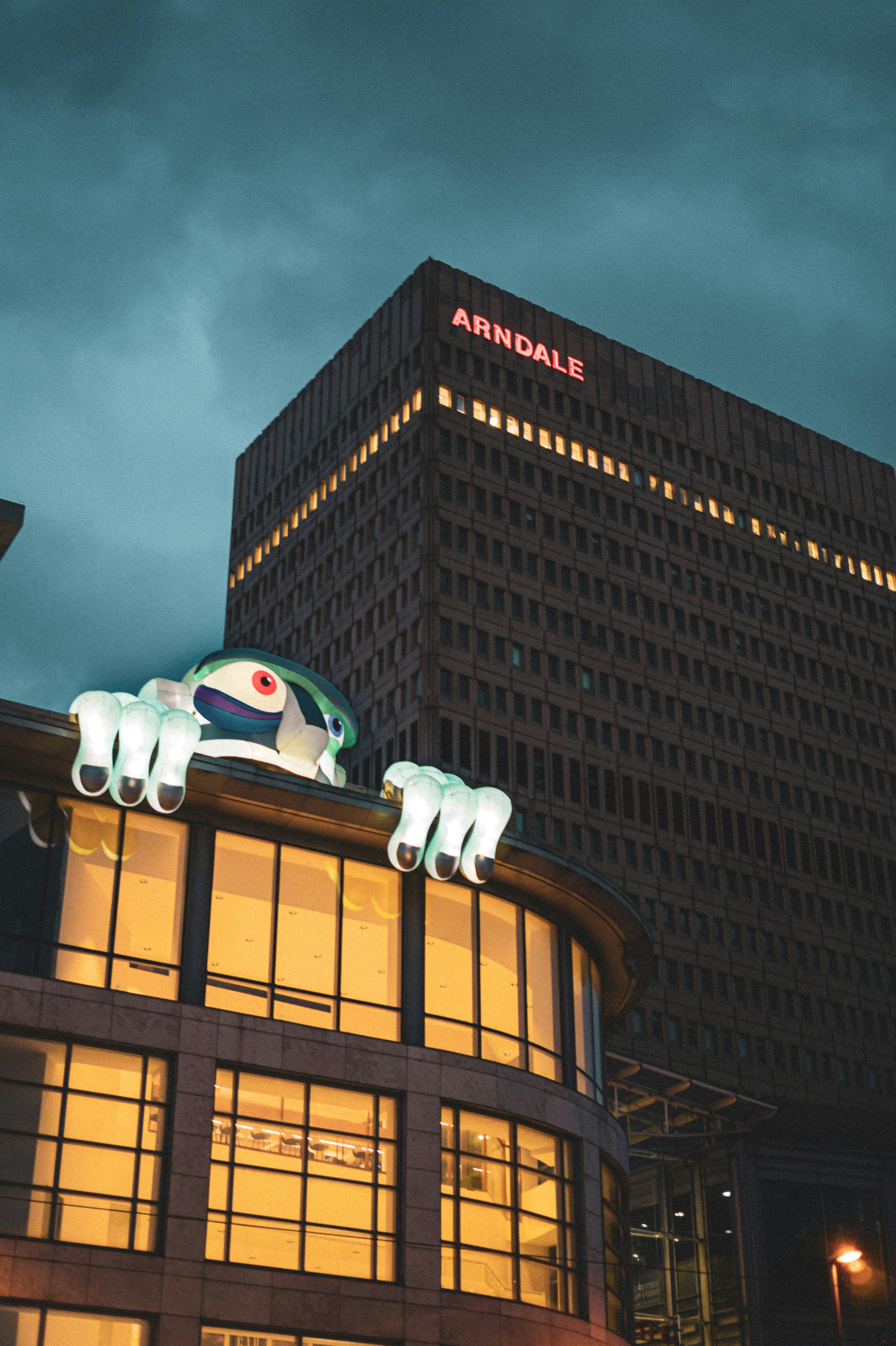 Cartoon monster on building roof with arndale sign at night.