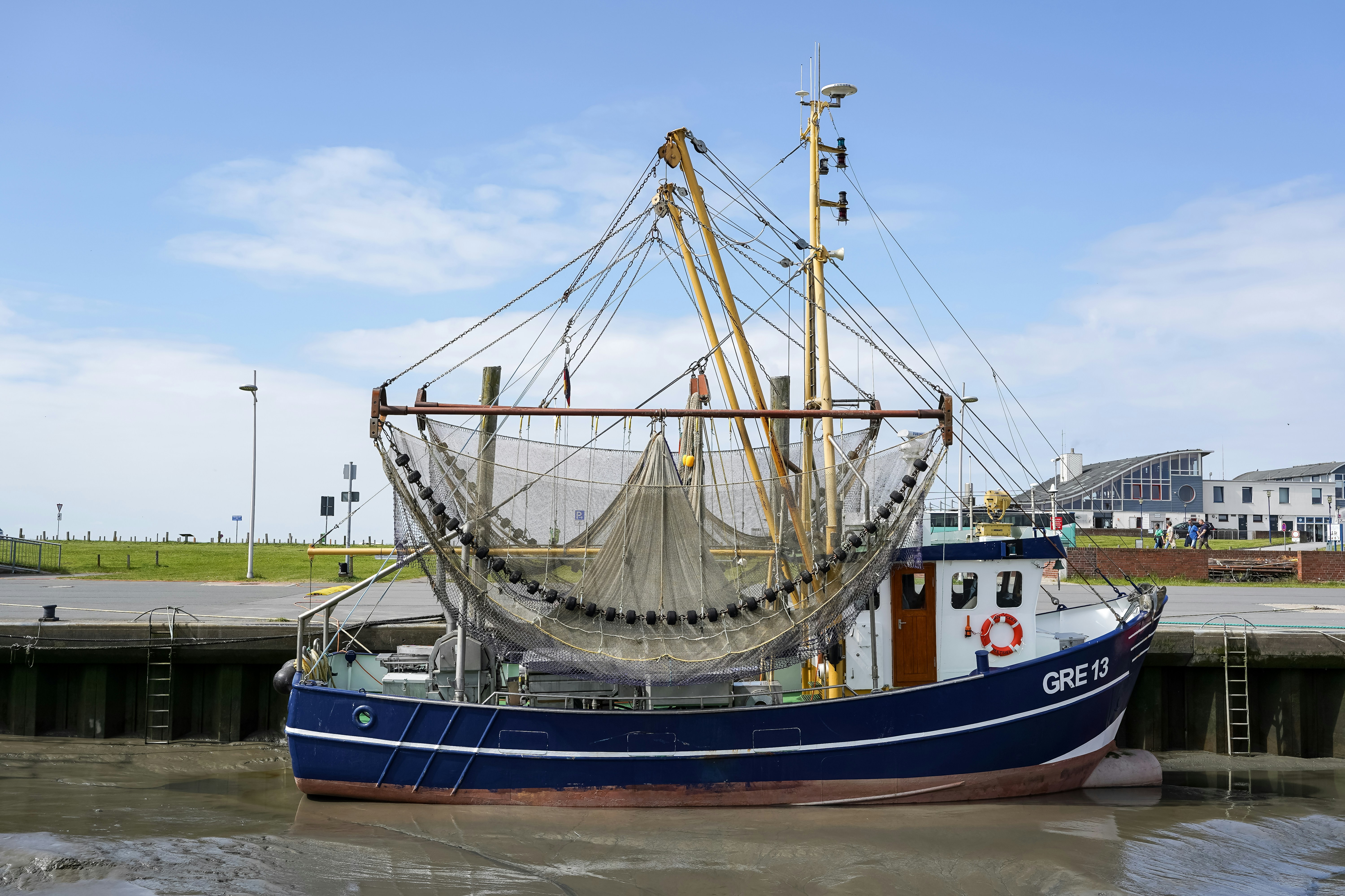 Blue fishing trawler at low tide with net rigging unfurled along a harbor wall