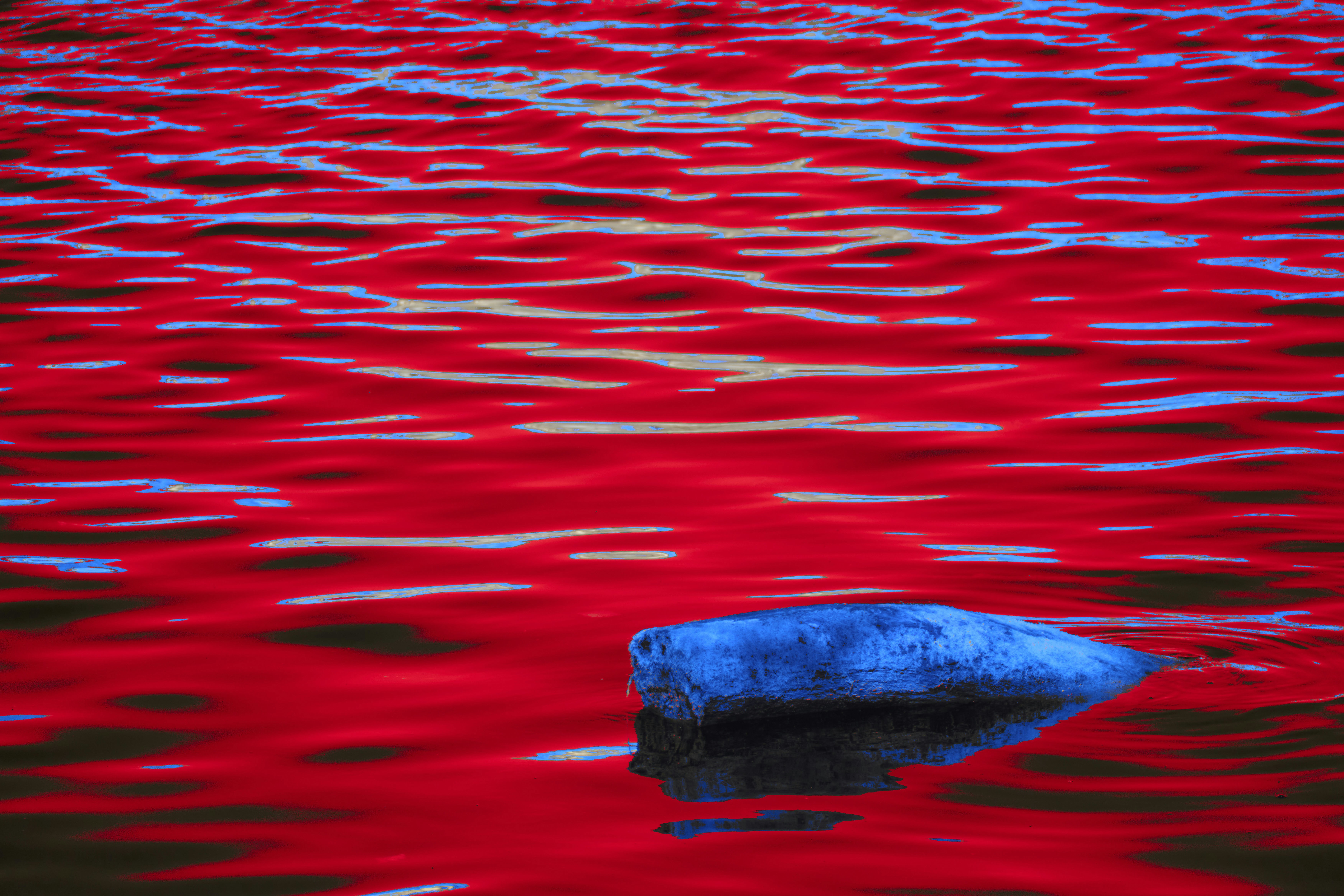 Crimson Ripples: A solitary stone drifting in surreal red tides