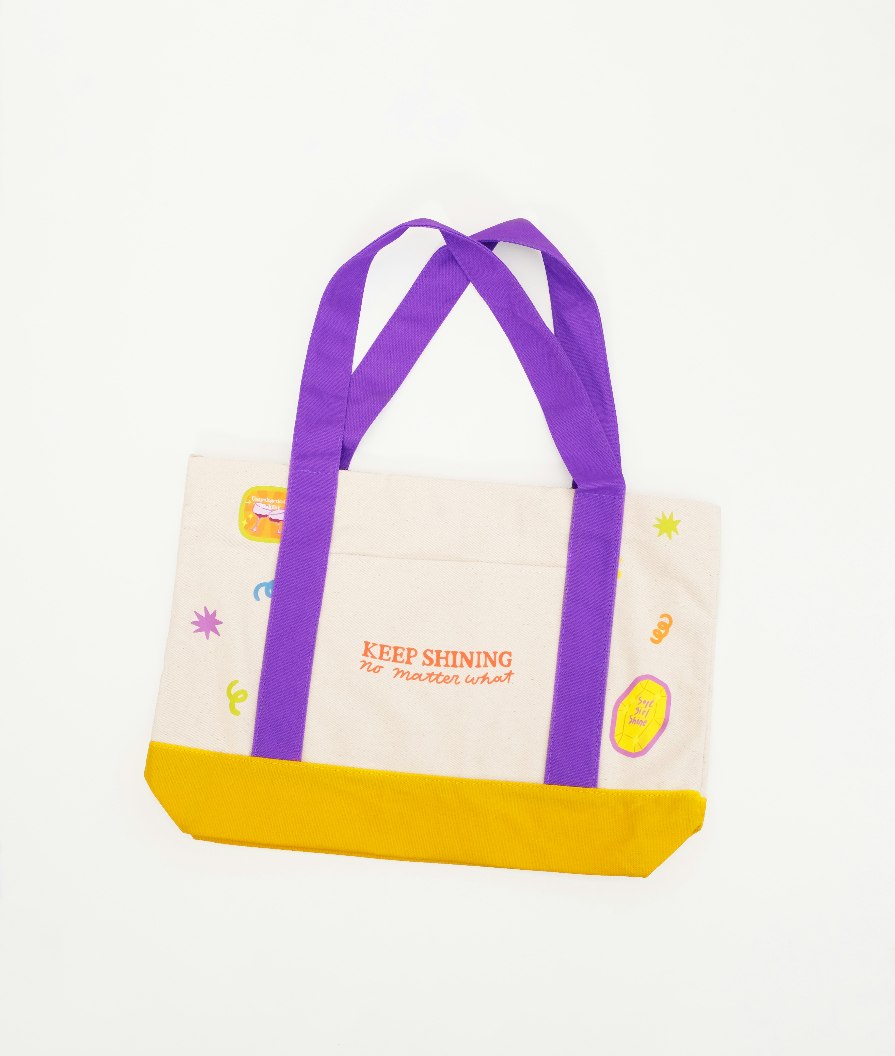 Bright canvas tote with purple handles and a yellow bottom panel, featuring playful graphics and text on a clean white background.