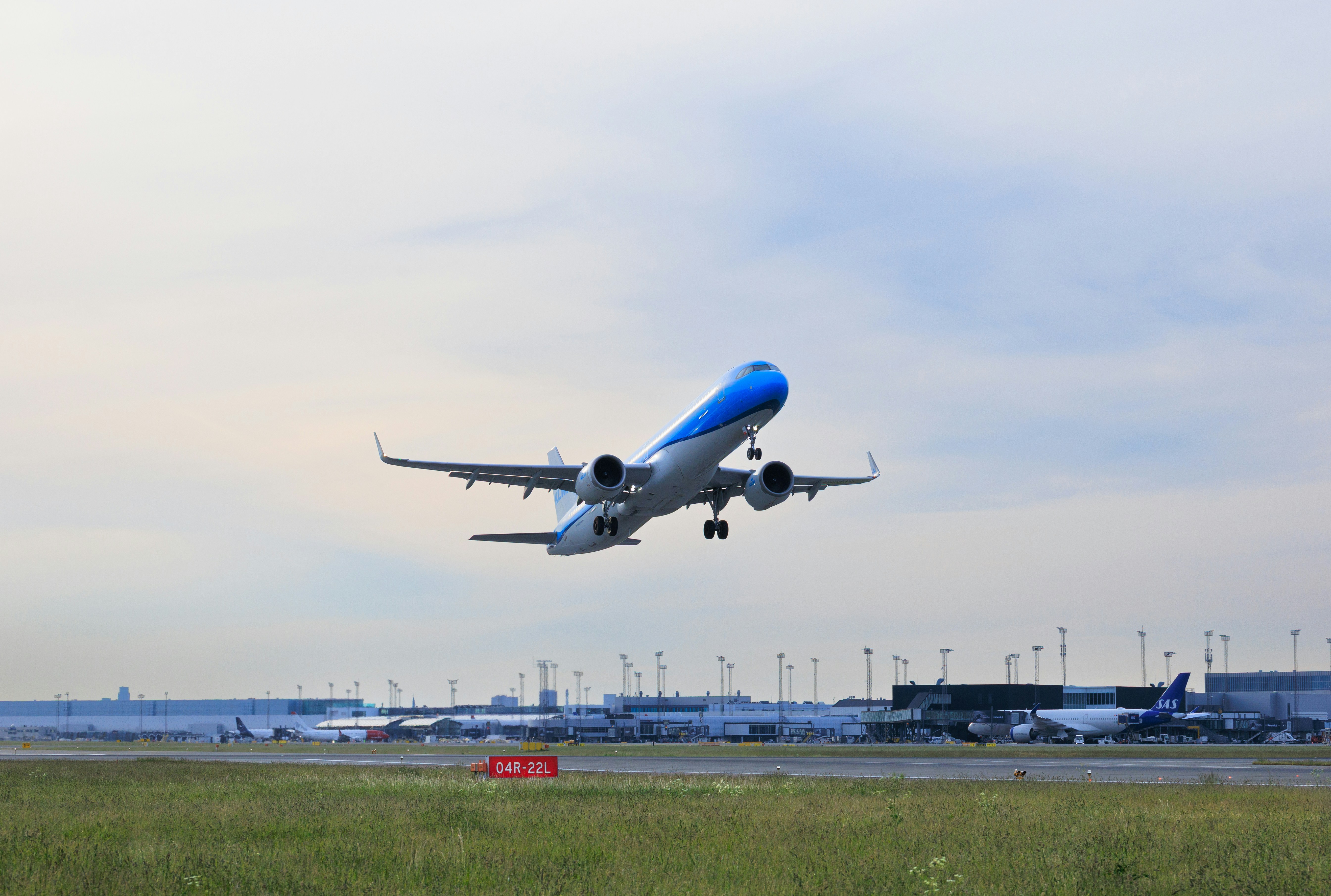 Blue-tailed Takeoff: Jet ascending above a quiet airport runway