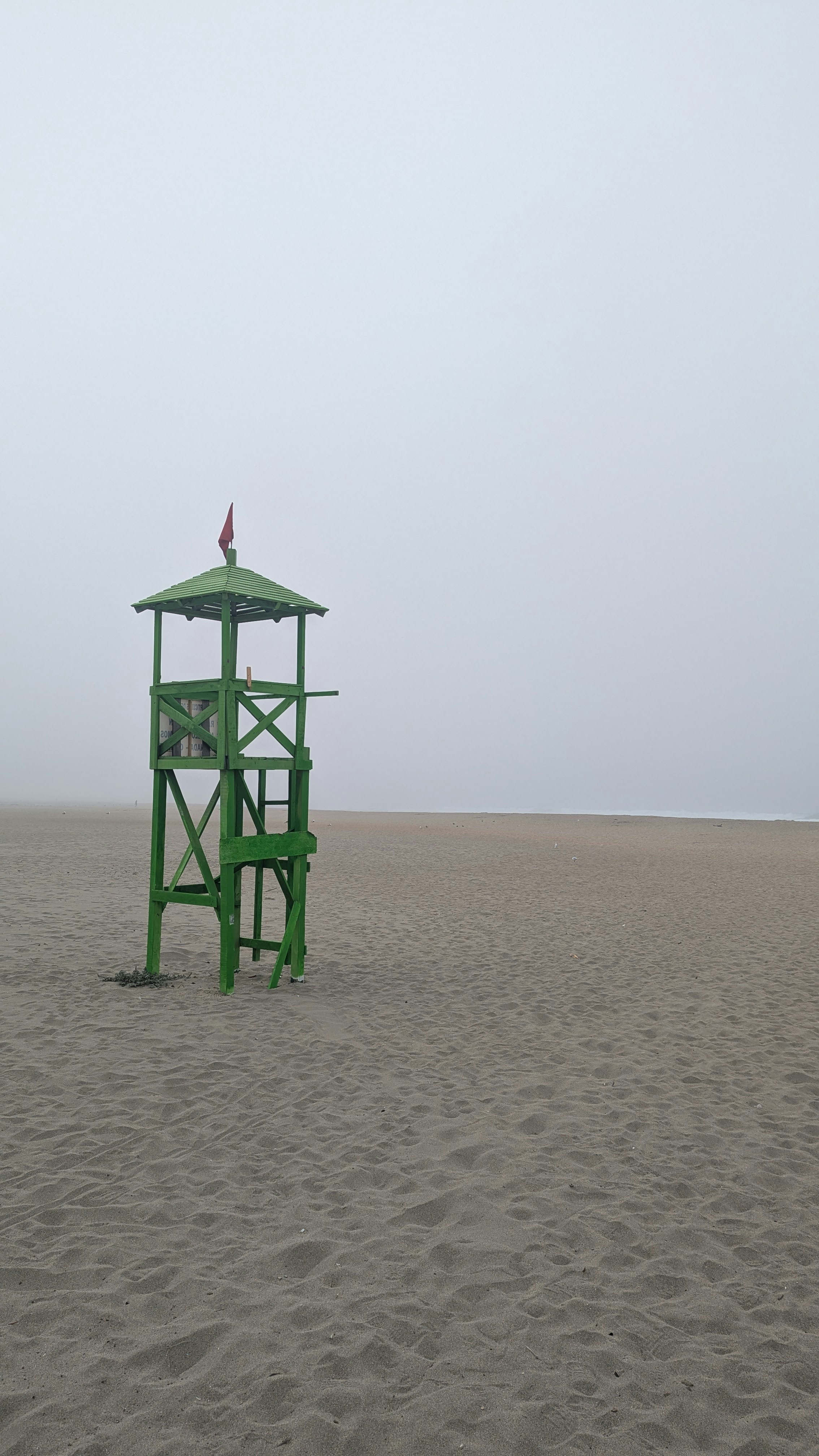 Green lifeguard tower on a foggy sandy beach.
