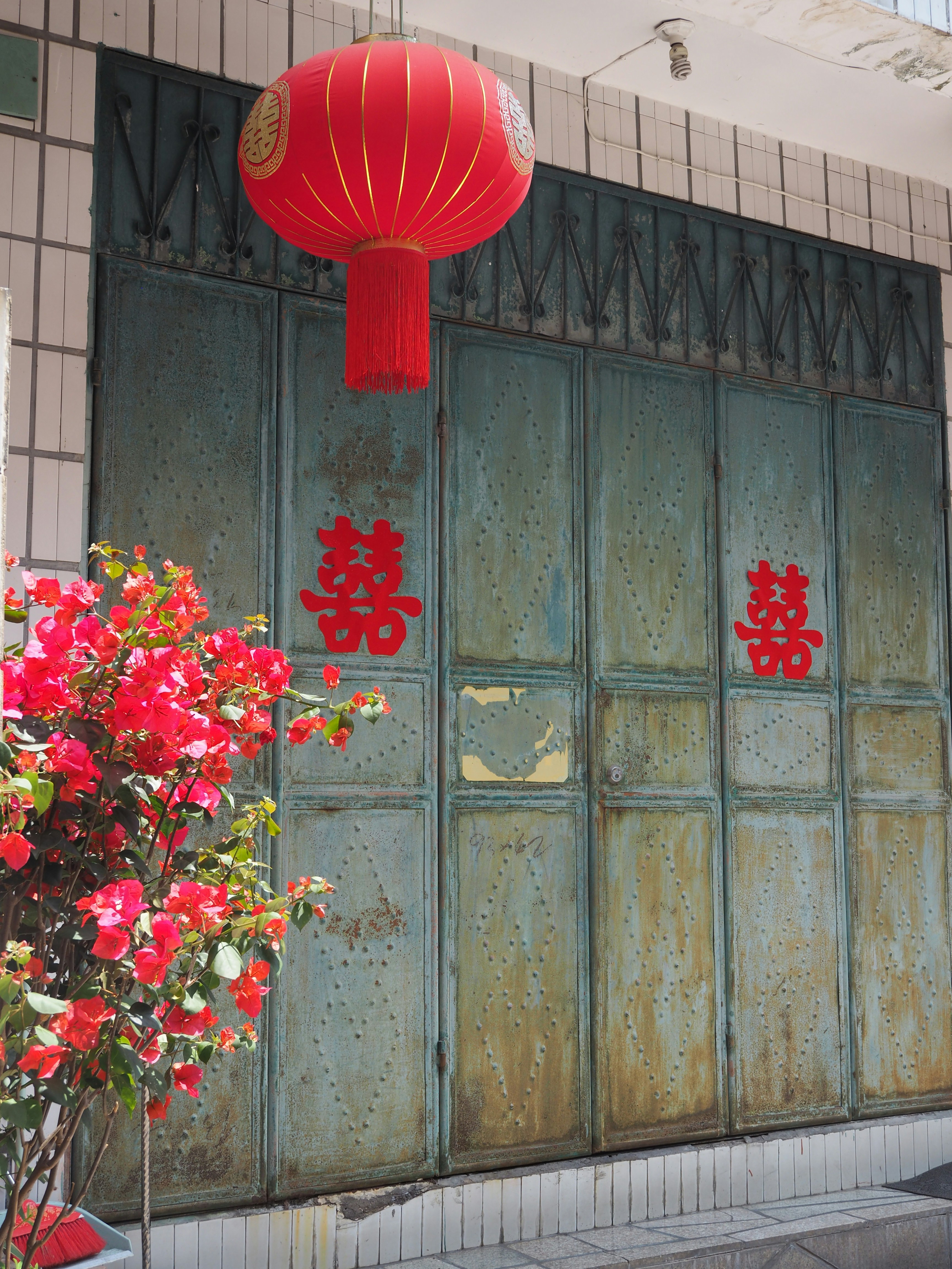 Red lantern and flowers decorate old green doors with characters.