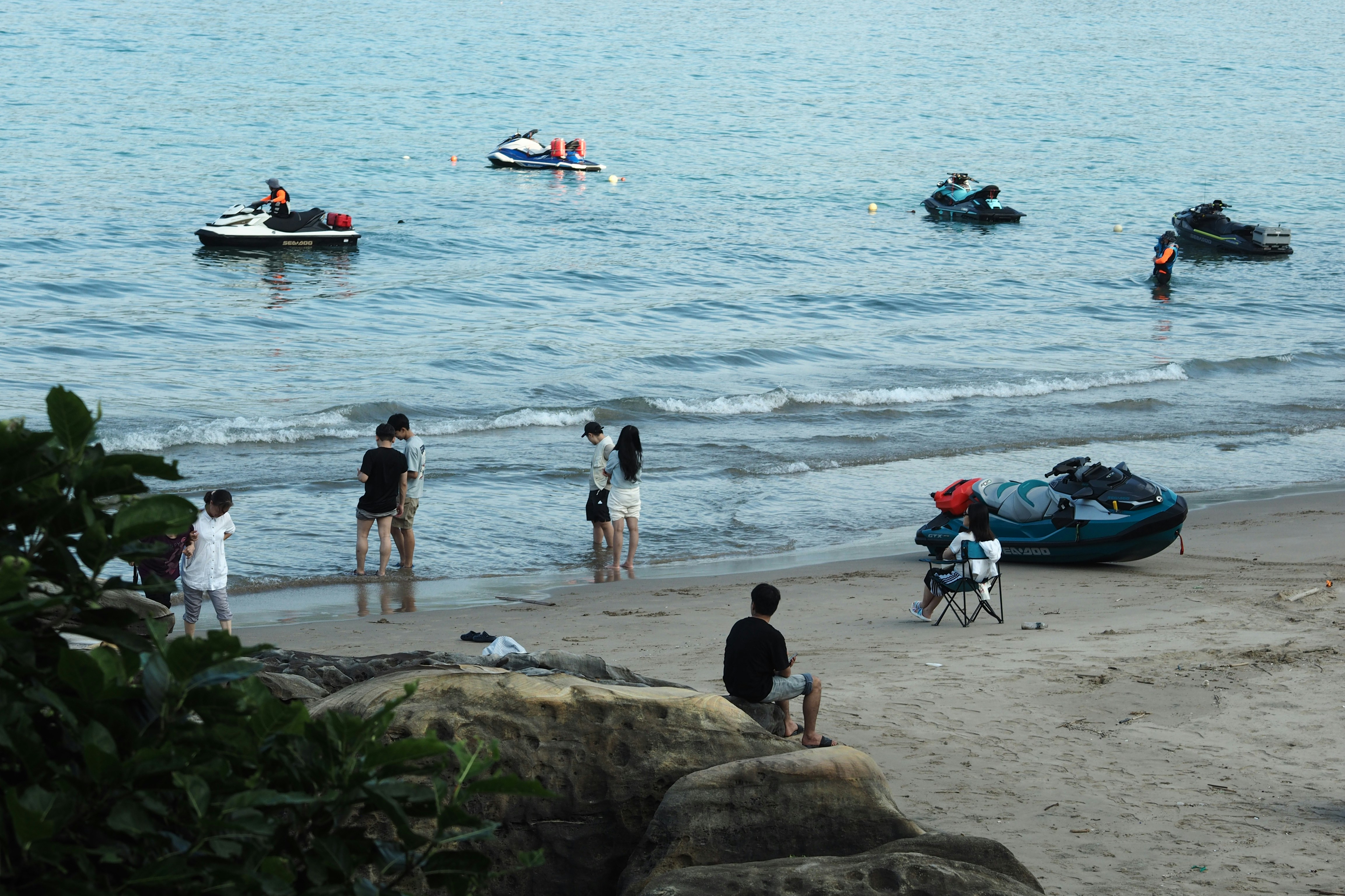 Beach Ensemble: People, Jetskis, and a Lone Angler at Dusk