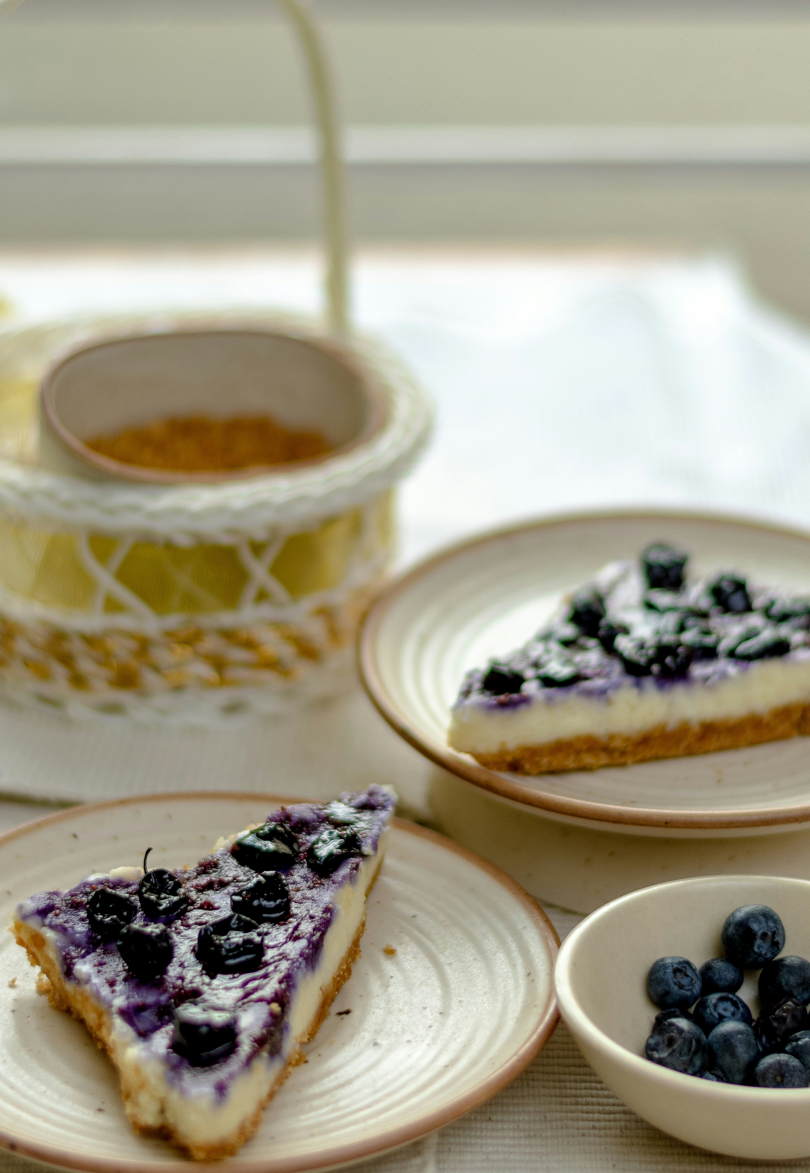 Blueberry cheesecake slices on a cozy kitchen table with a lace basket in the background