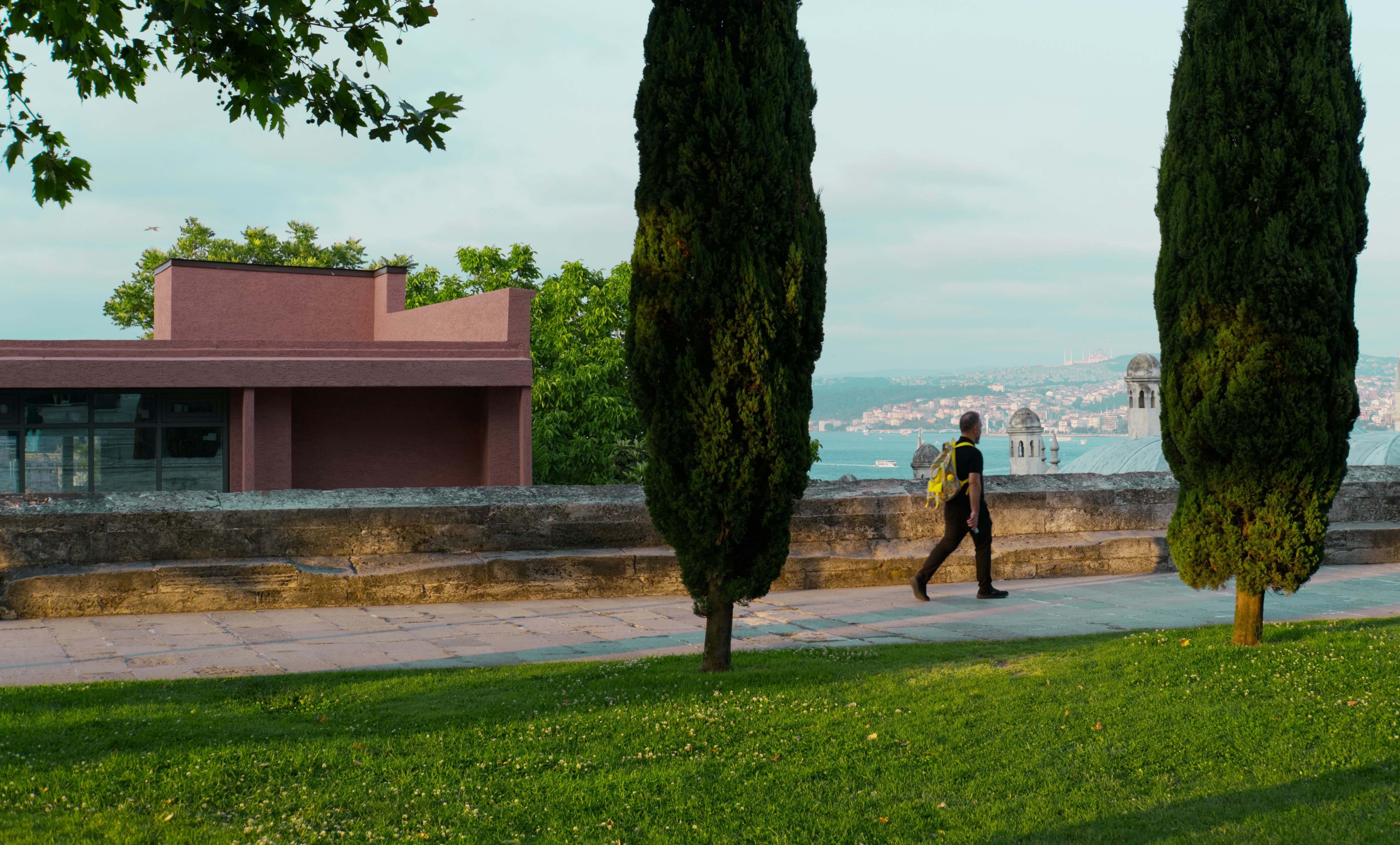 Traveler in a sunlit riverside park past a pink pavilion