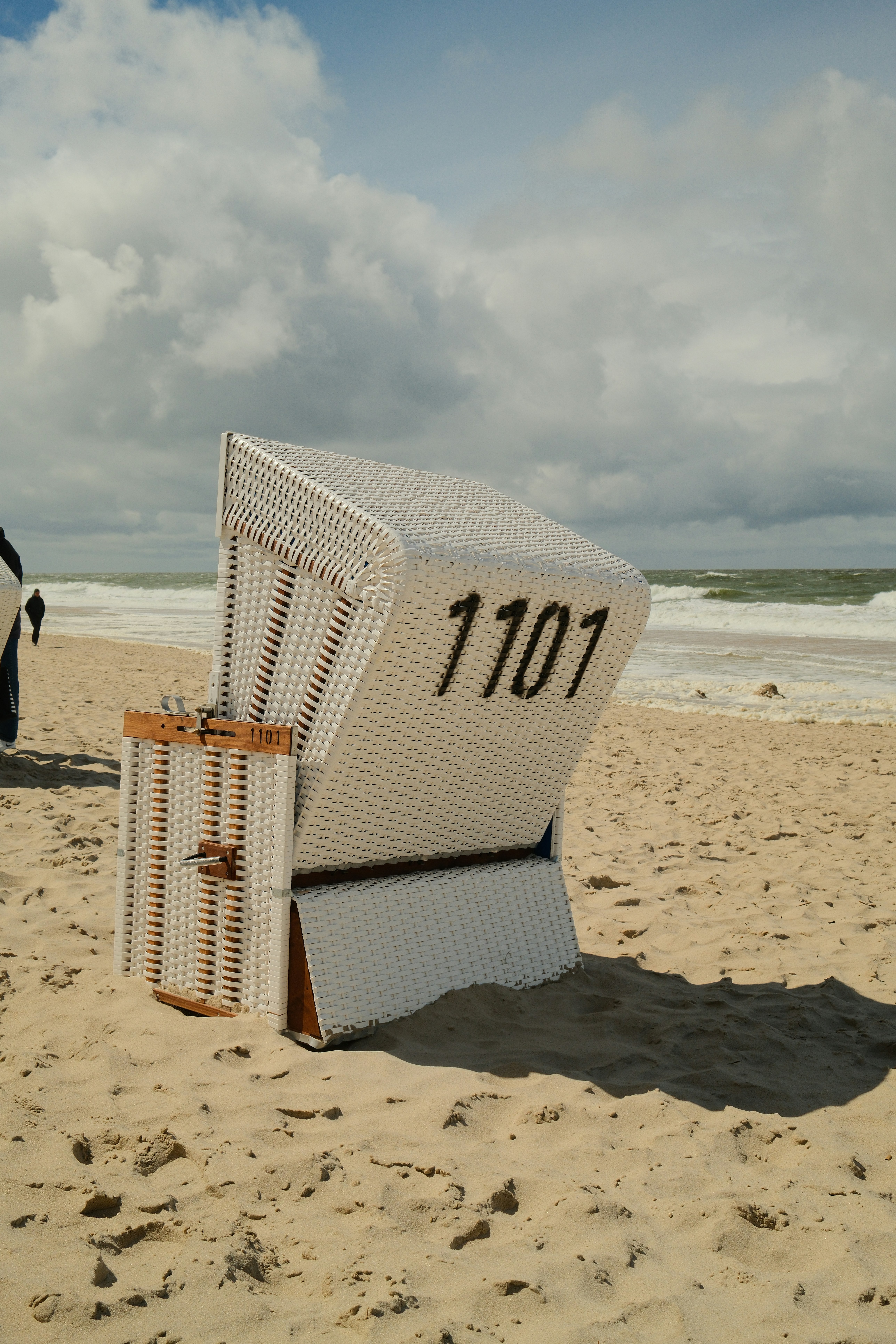 A white wicker beach chair "1101" on a sandy beach.