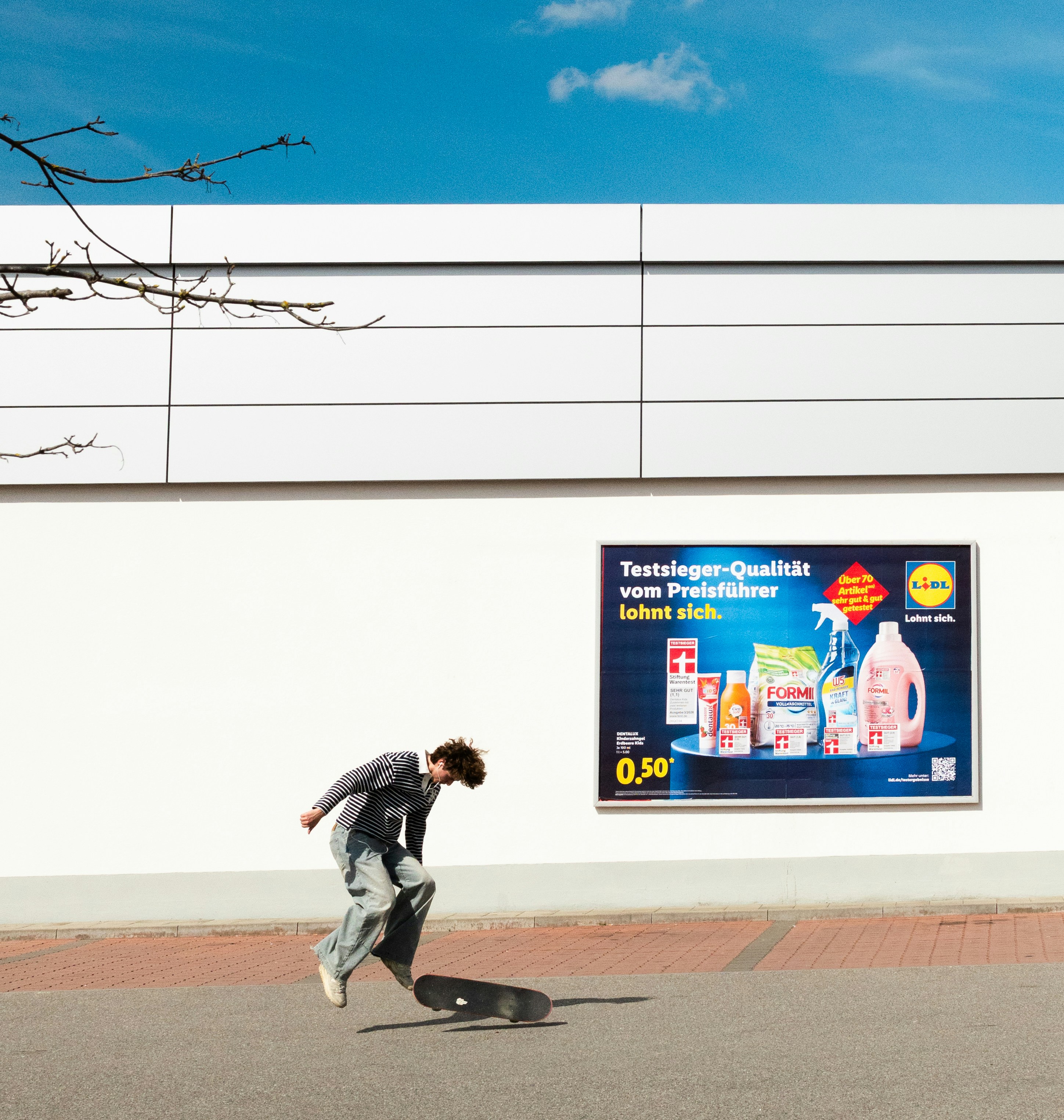 Skateboarder in Motion Along a White Wall with an Advert