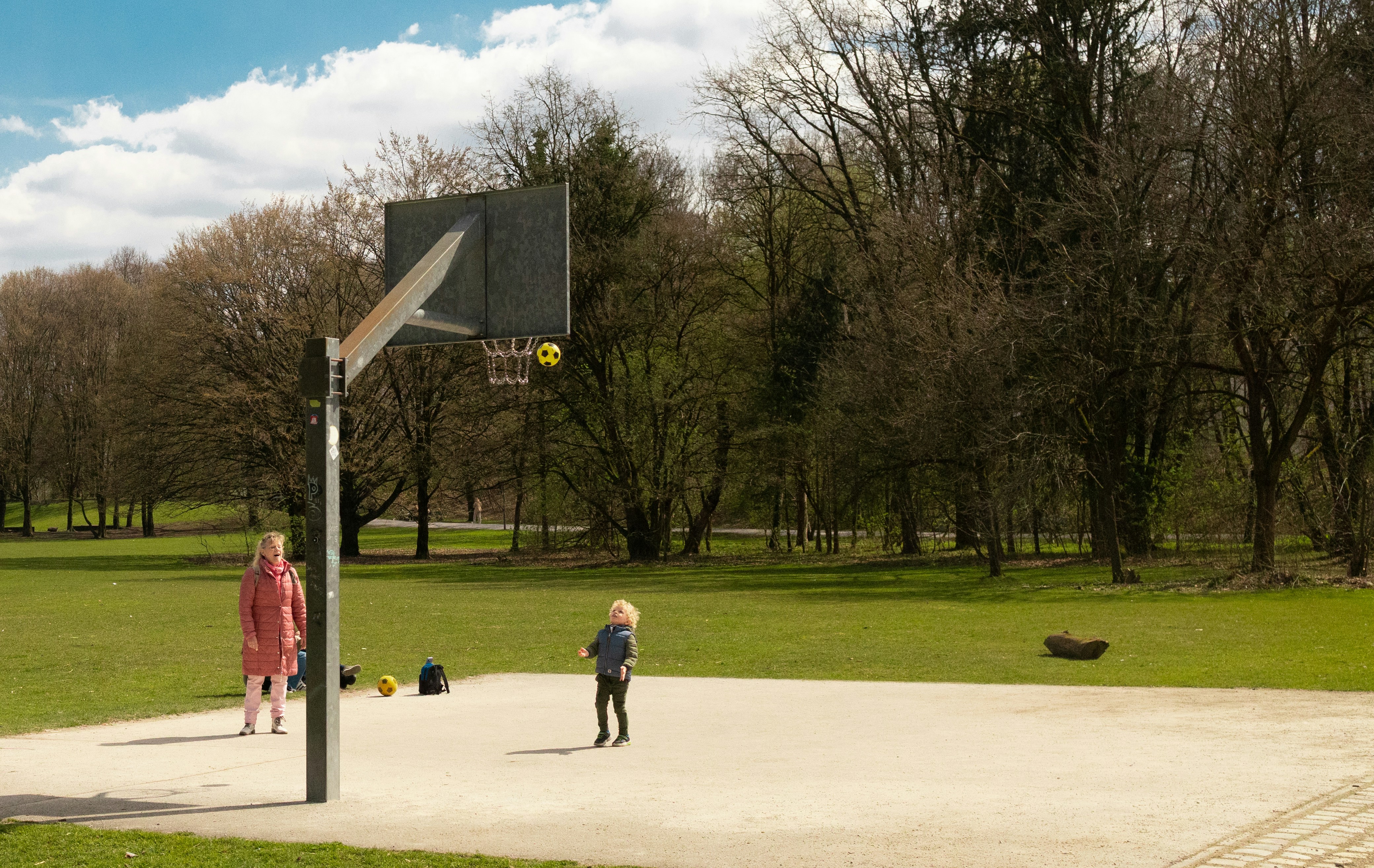 Child with basketball under a distant hoop on a sunlit park court