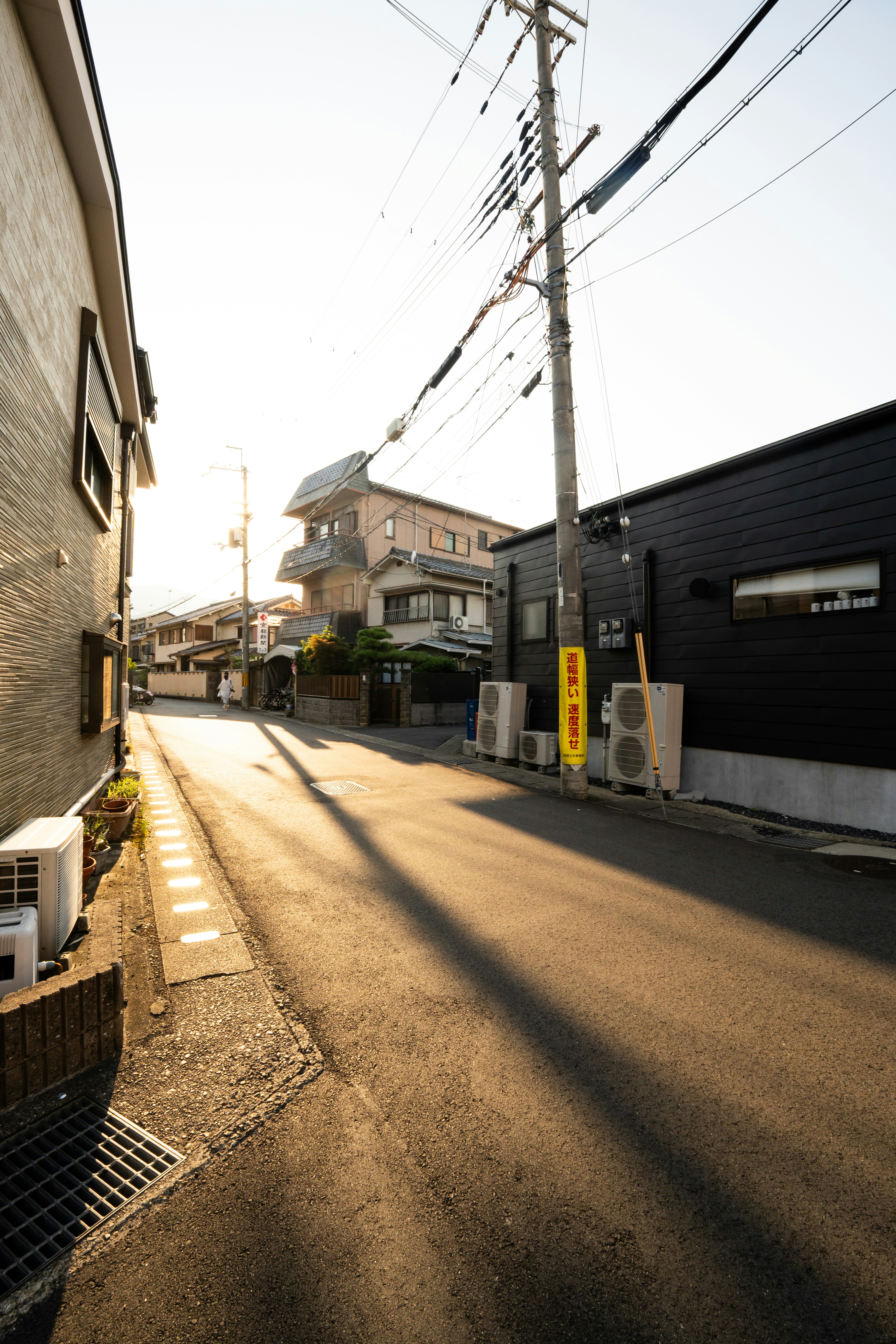 Sunny street with long shadows, buildings, and utility poles.
