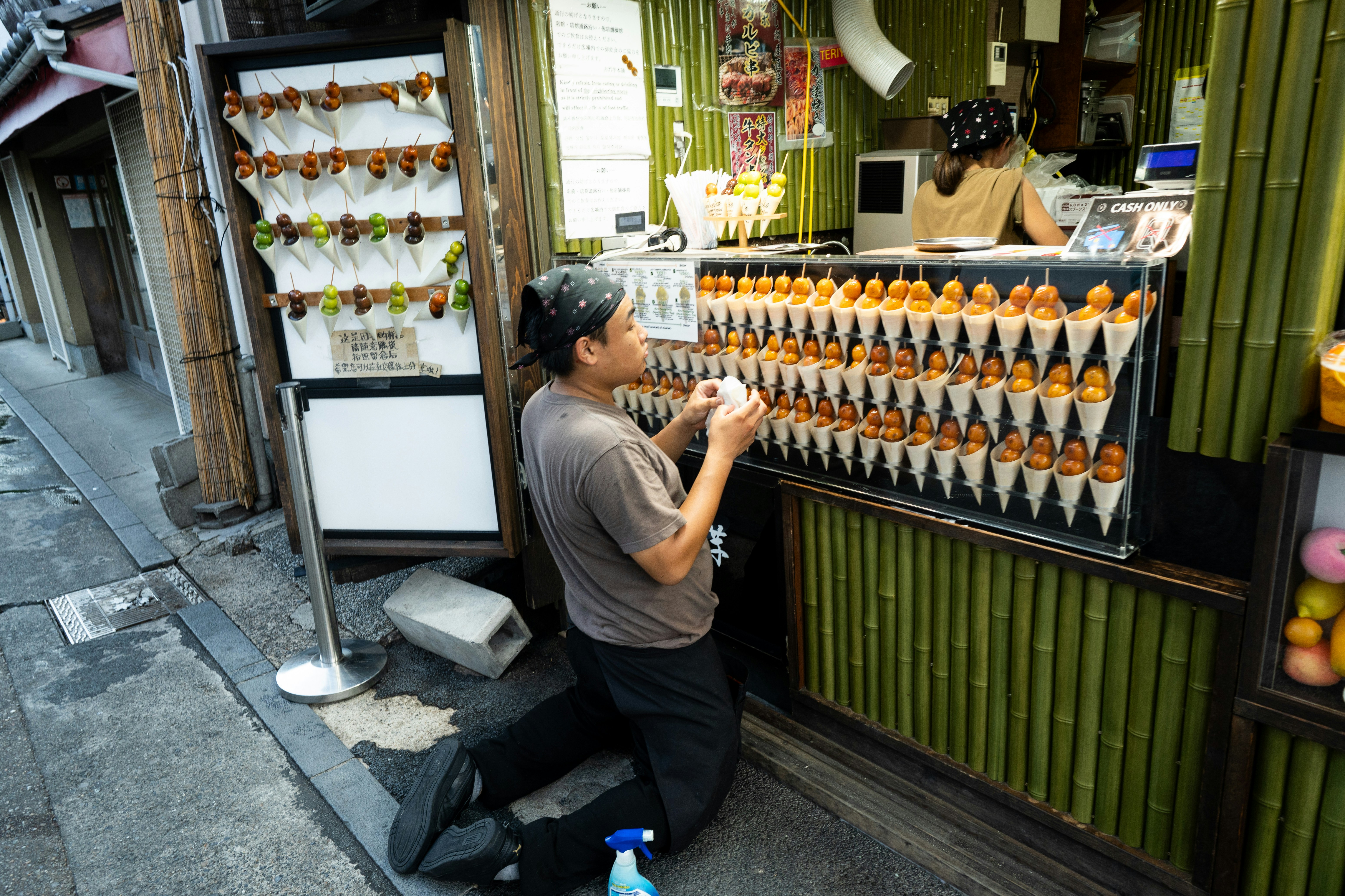 Kneeling Vendor Aligns Pearls of Orange Cones at a Street Snack Stand