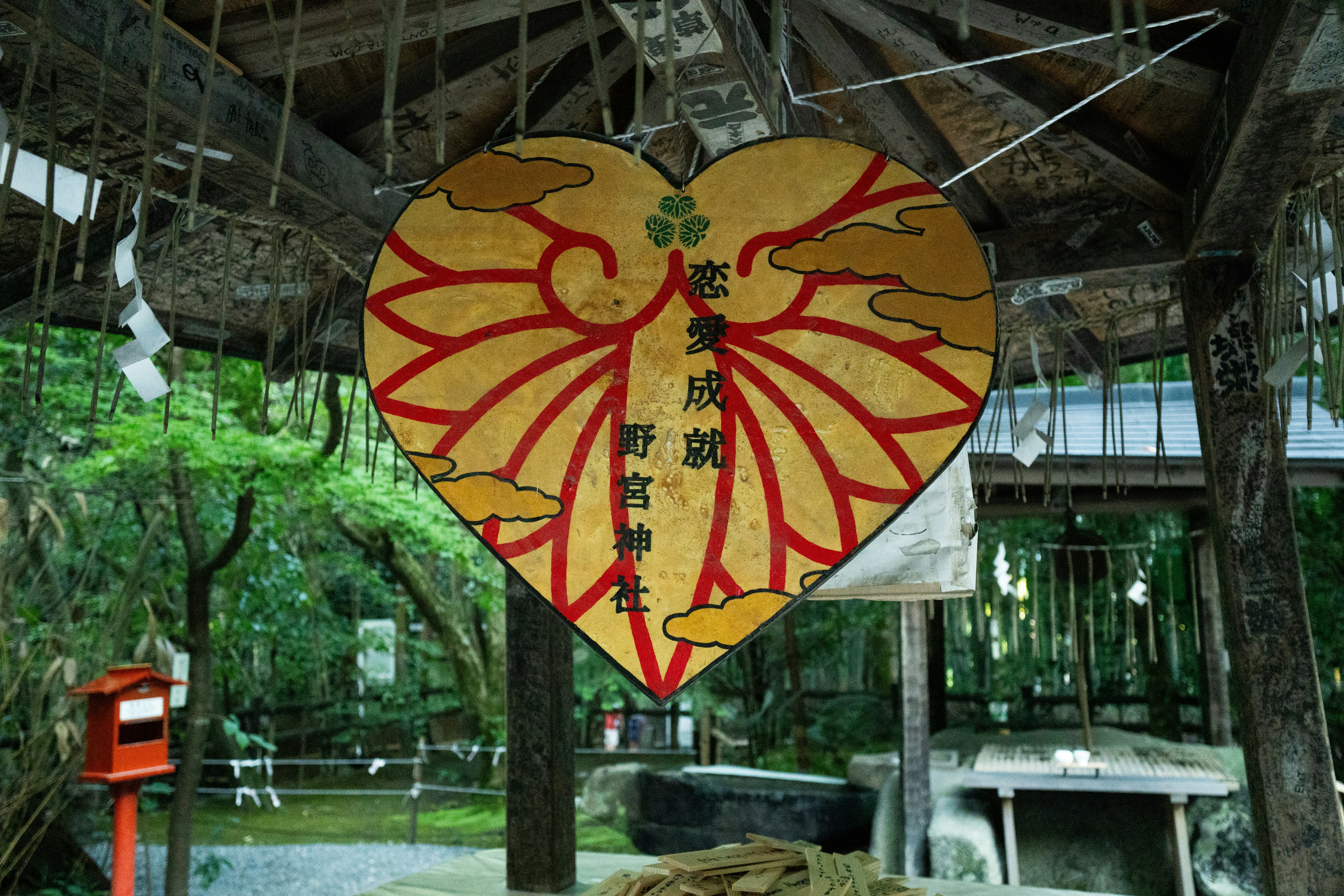 Heart-shaped wooden plaque with japanese characters in a temple setting.