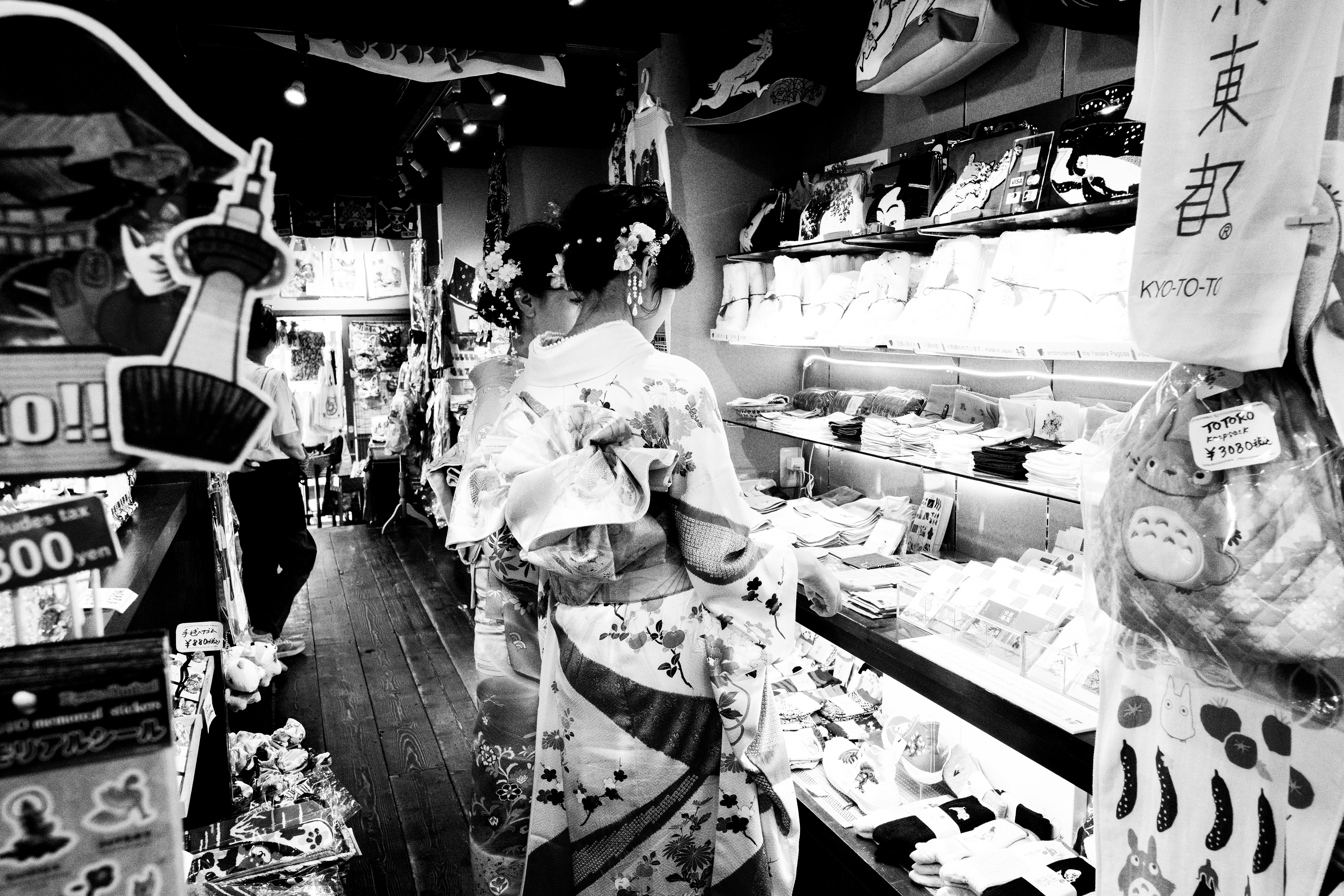 Shopper in traditional kimono examines goods in a store.