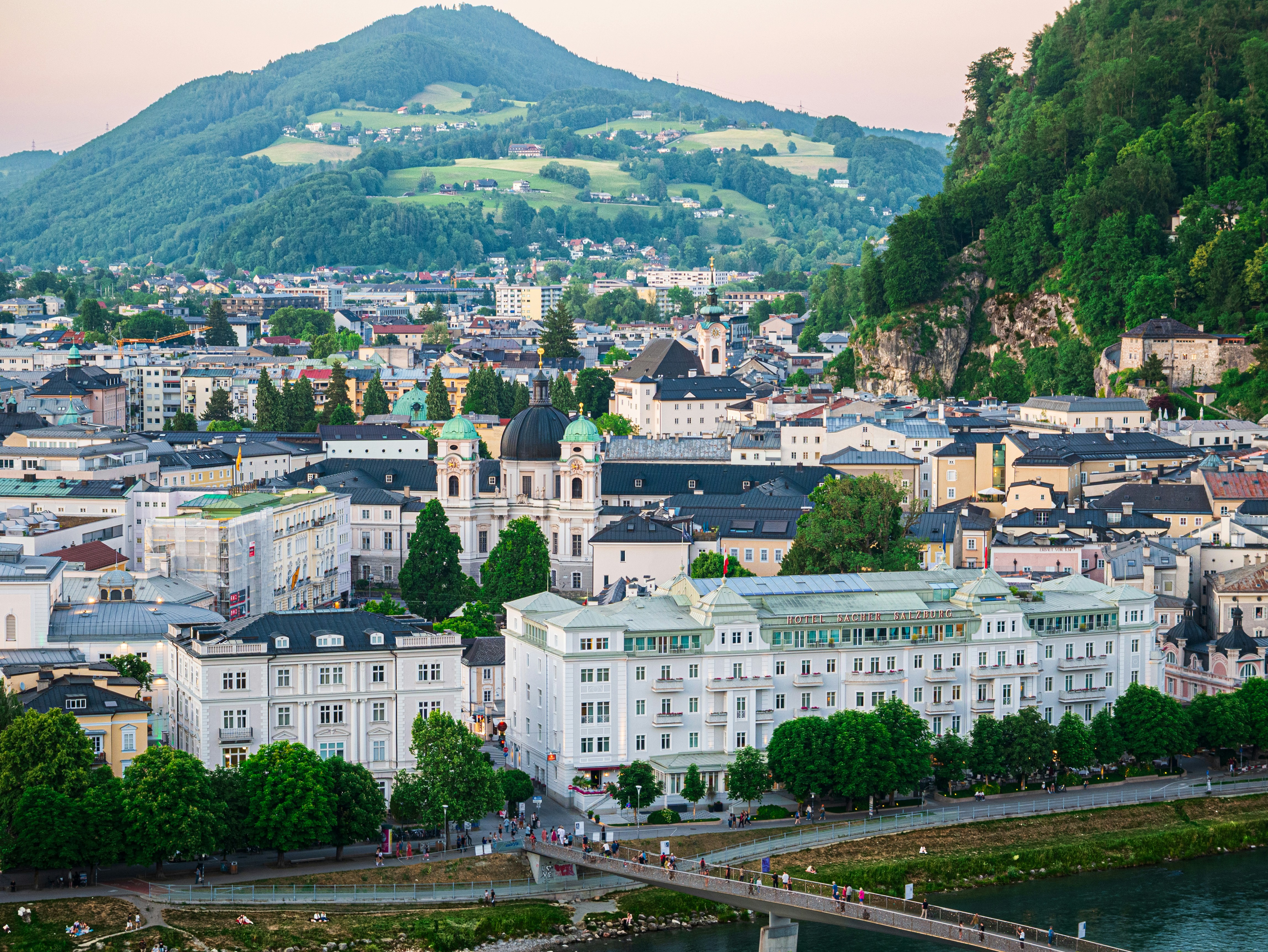 Historic salzburg cityscape with river and green mountains.